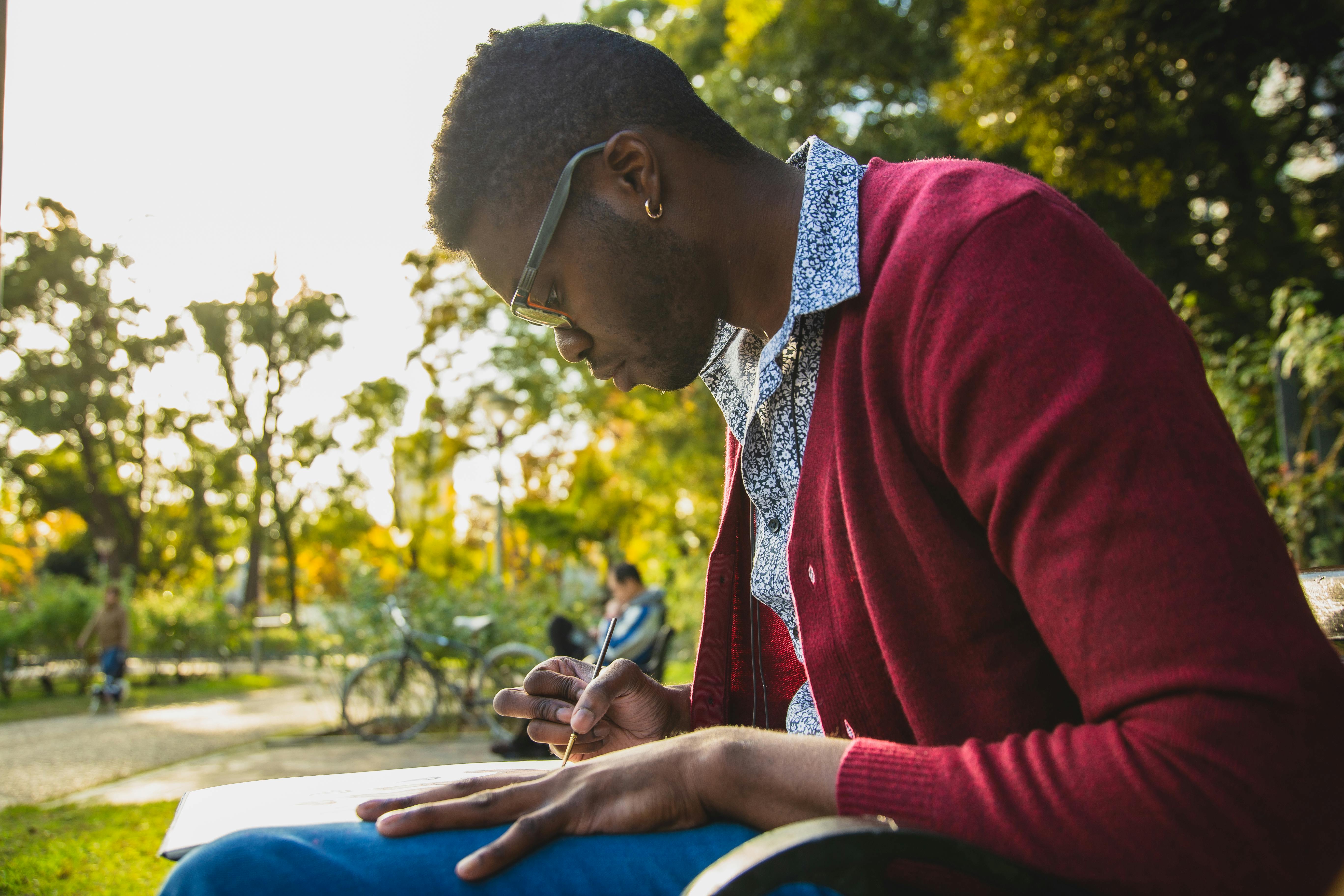Black student writing on paper while studying in park · Free Stock Photo