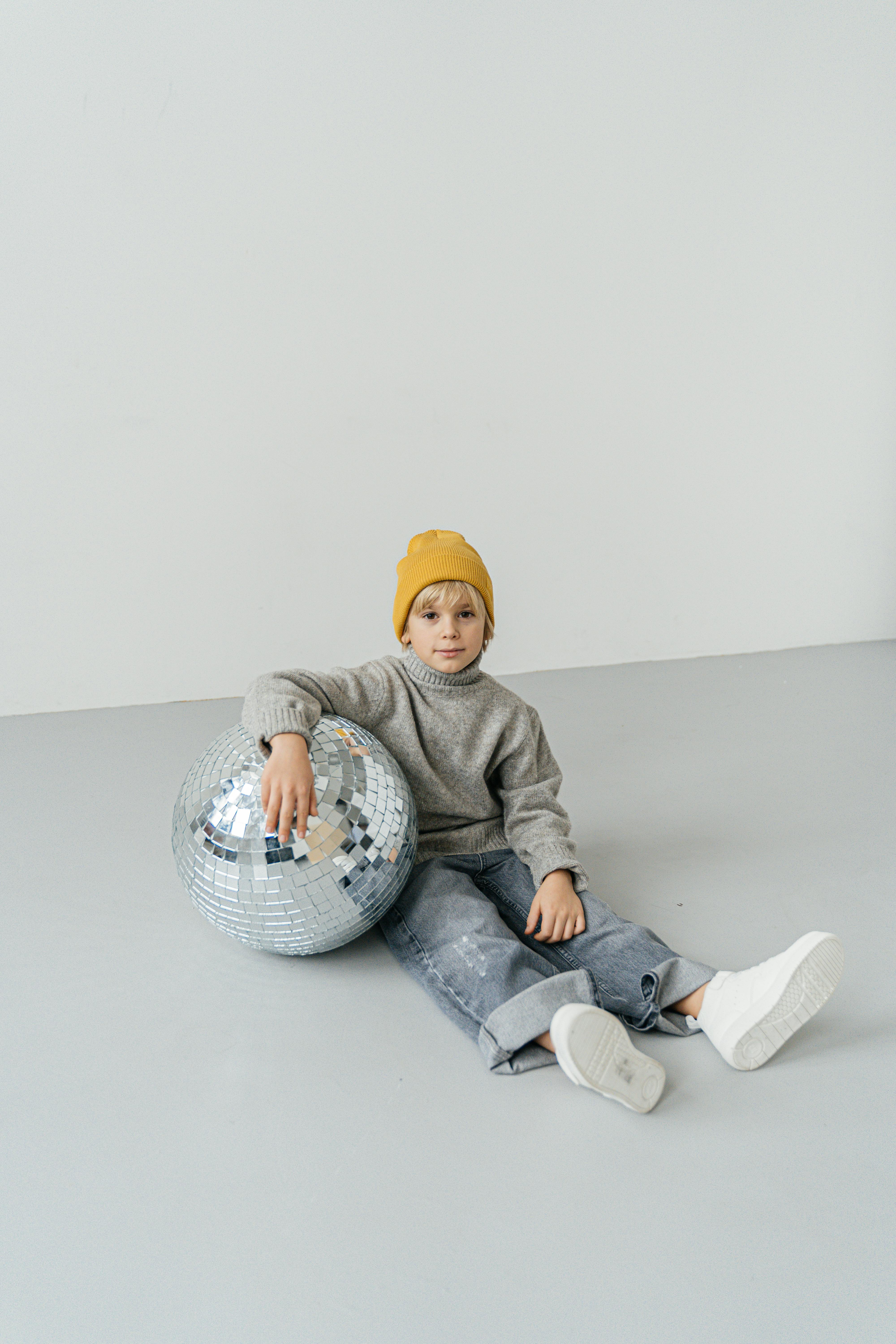 A Boy Wearing a Bonnet and Sitting Next to a Disco Ball · Free Stock Photo