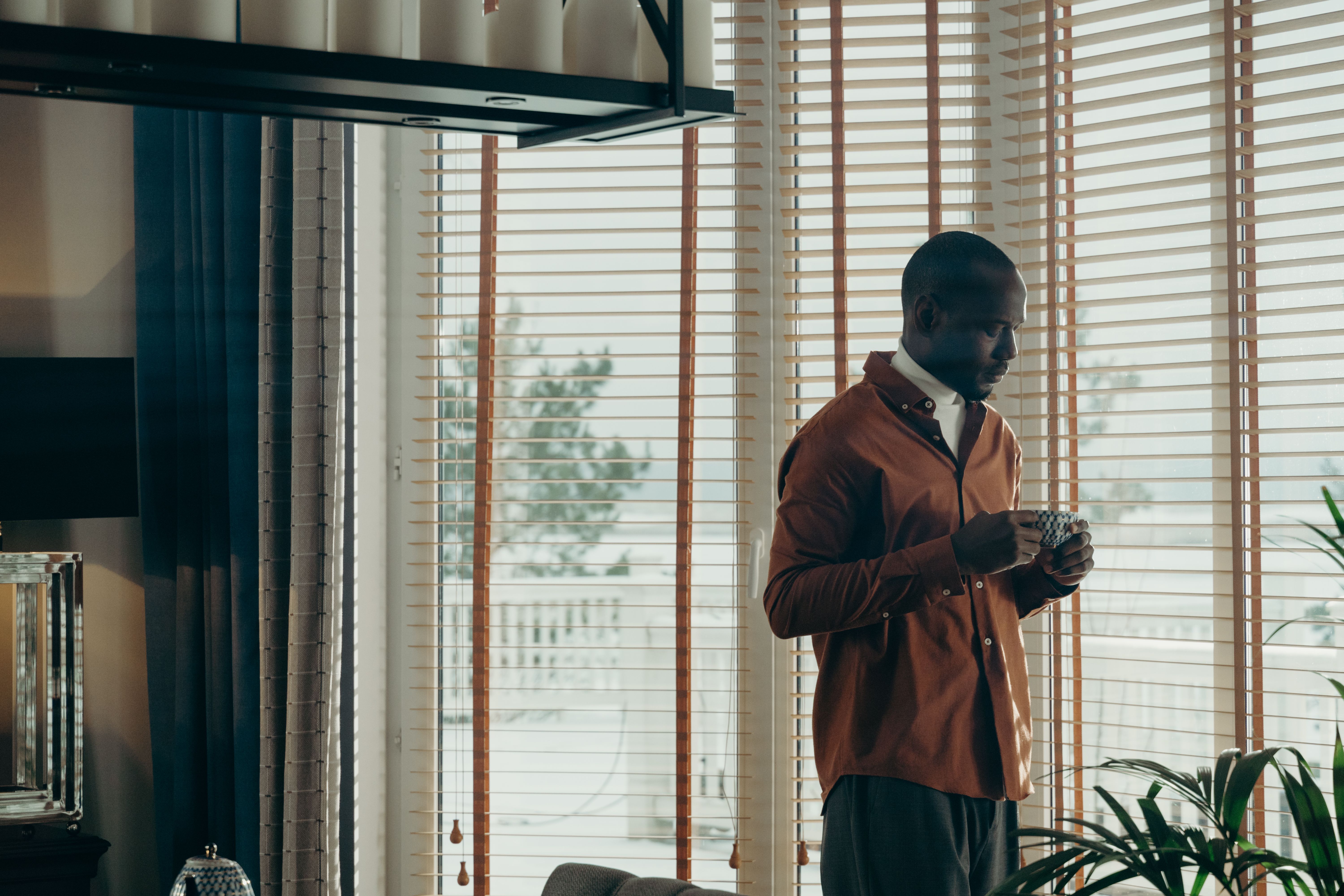 Man Standing Near the Window with Wooden Blinds · Free Stock Photo