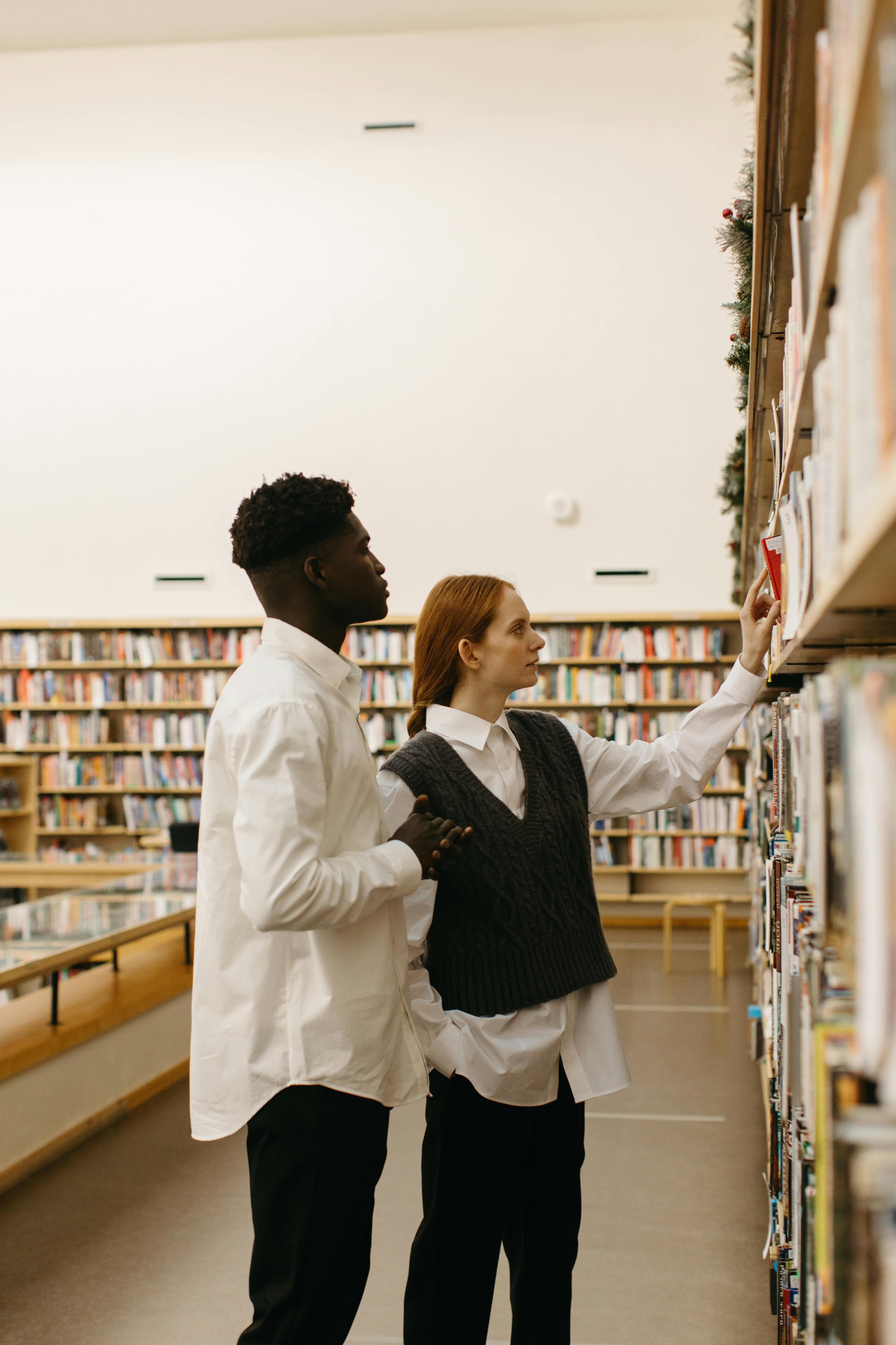 A Man and Woman Looking at the Bookshelves Inside the Library · Free ...