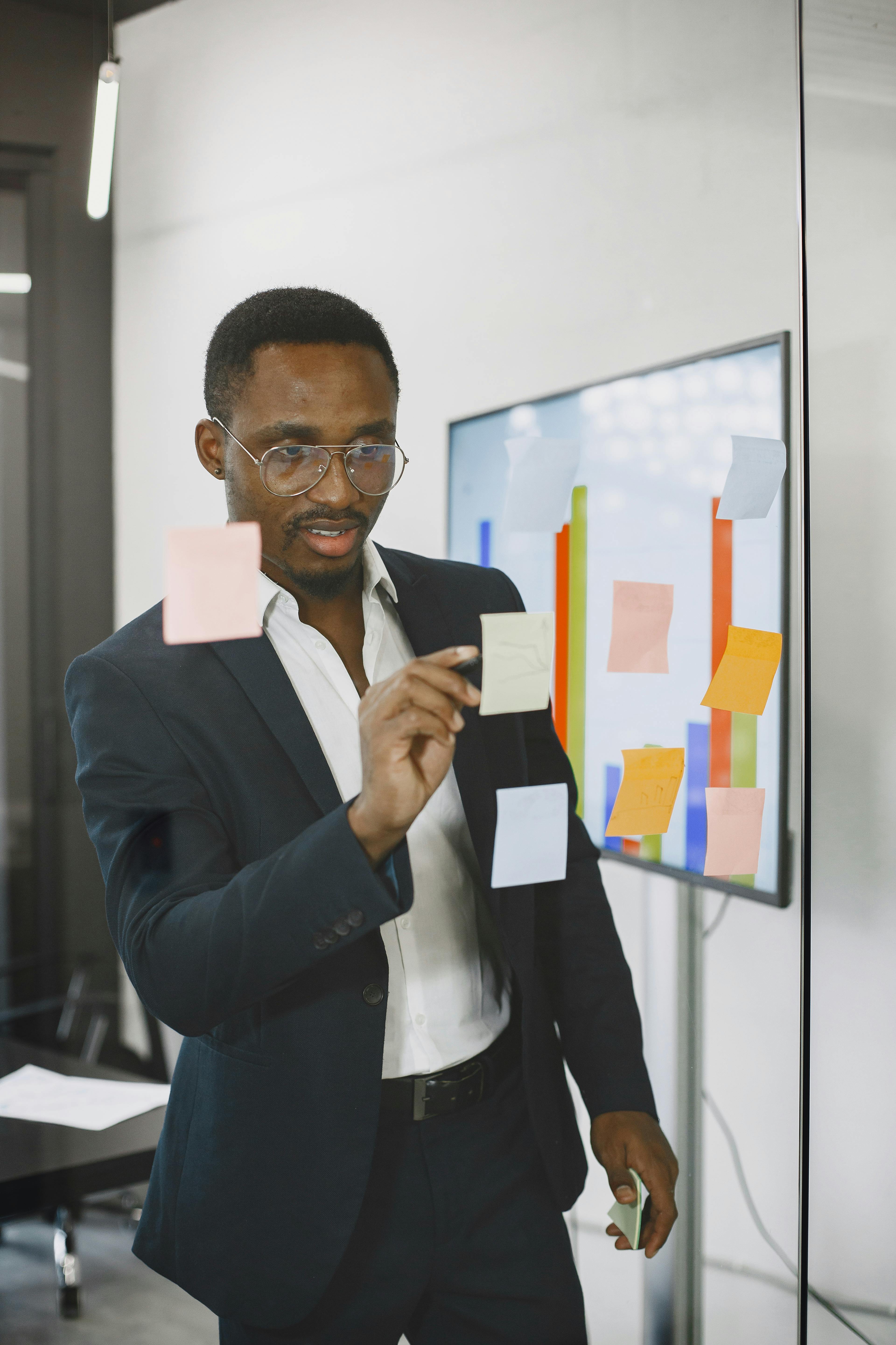 A Man in Black Suit Putting Sticky Notes on Glass Wall · Free Stock Photo