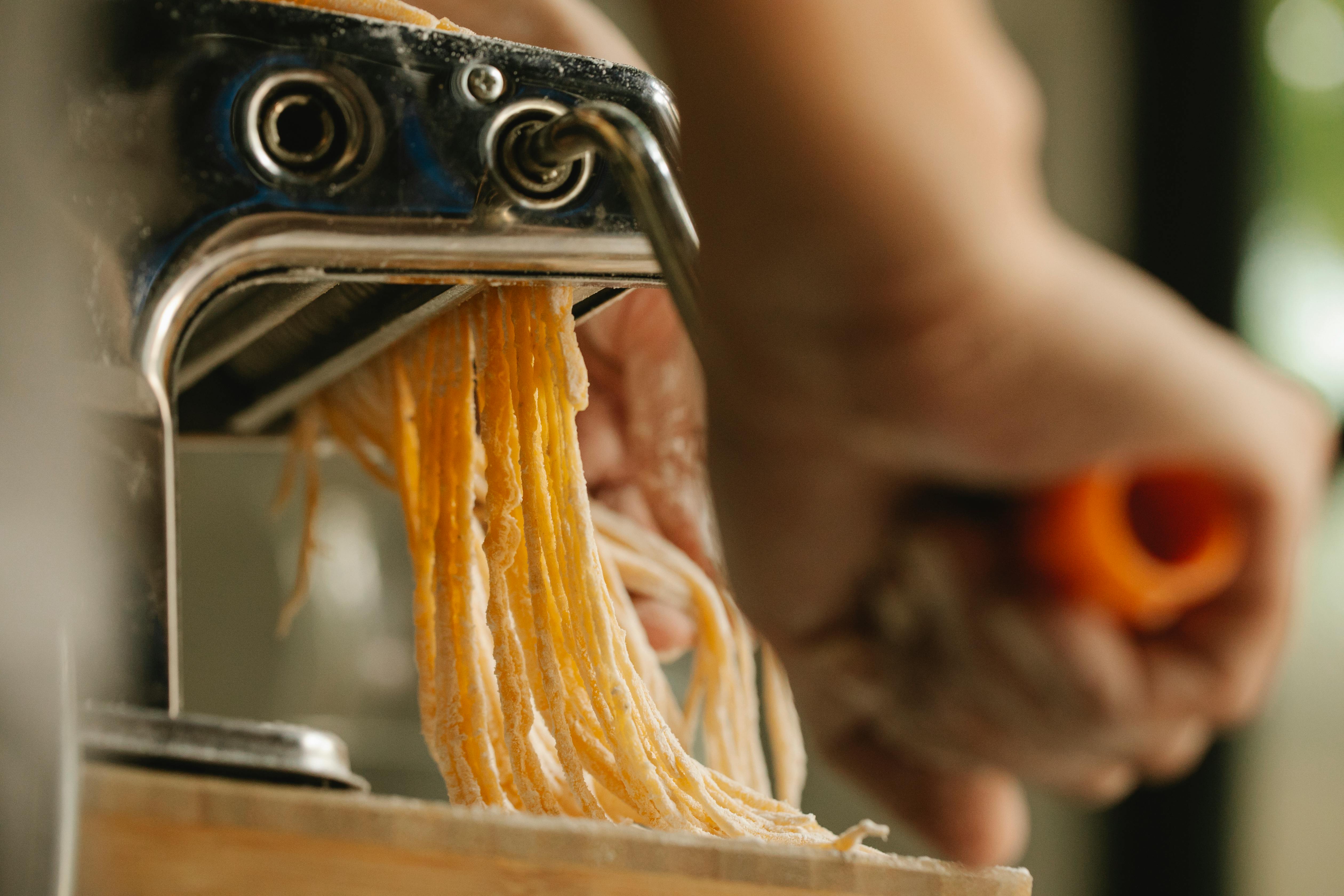 Crop person cutting dough with pasta machine · Free Stock Photo