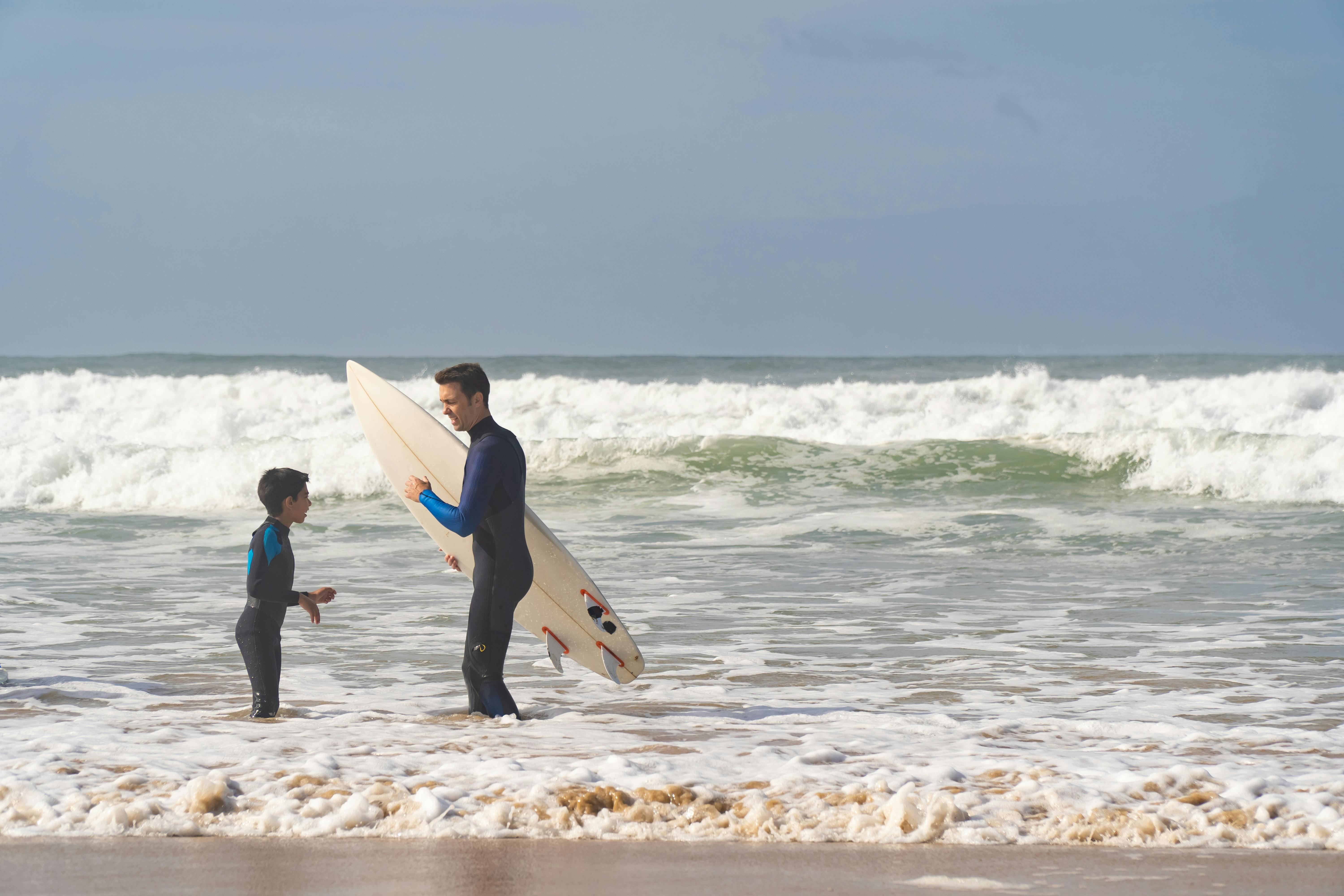 Man Holding Surfboard While Talking to a Boy at the Beach · Free Stock ...