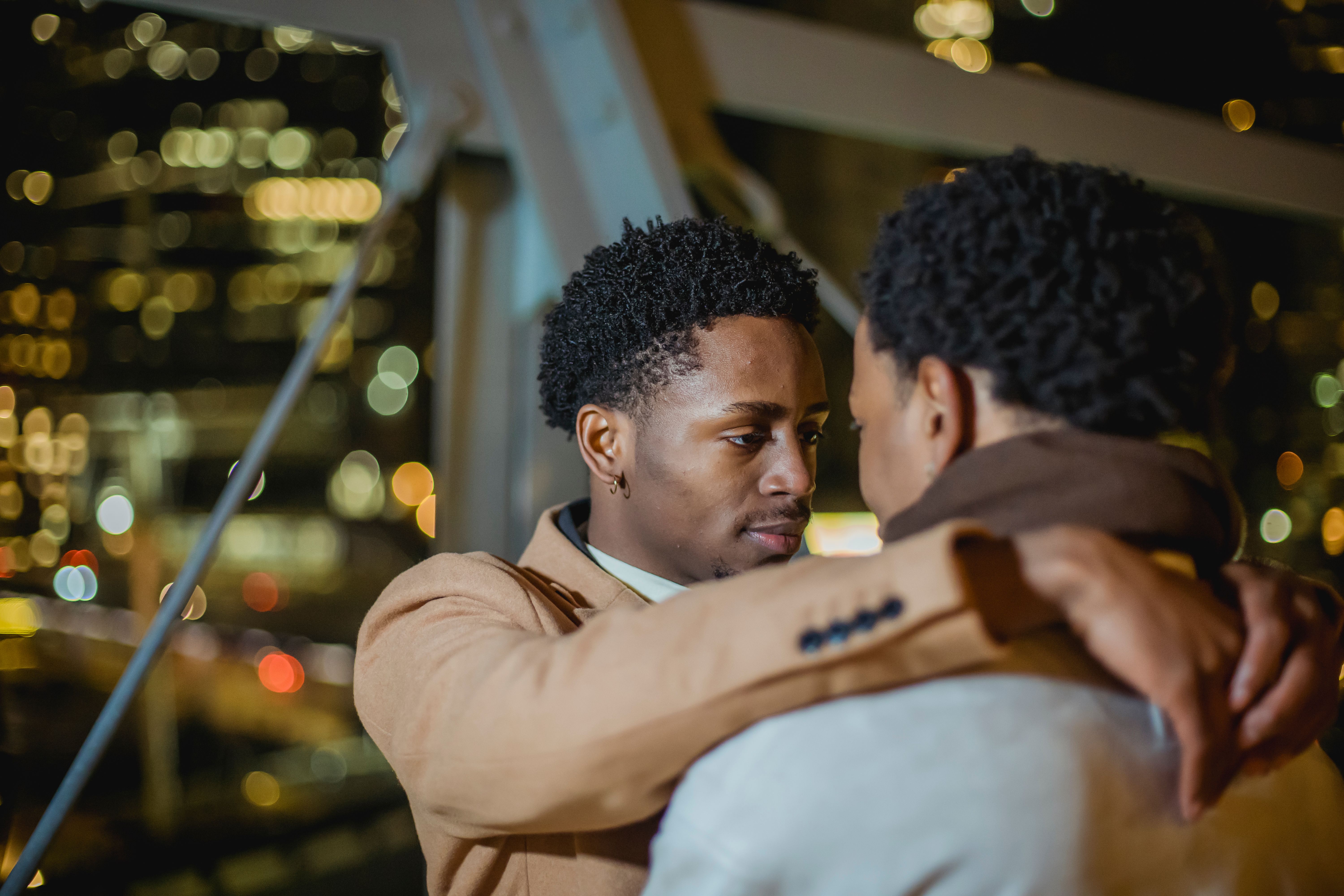 Black homosexual male couple cuddling in glowing city street · Free ...