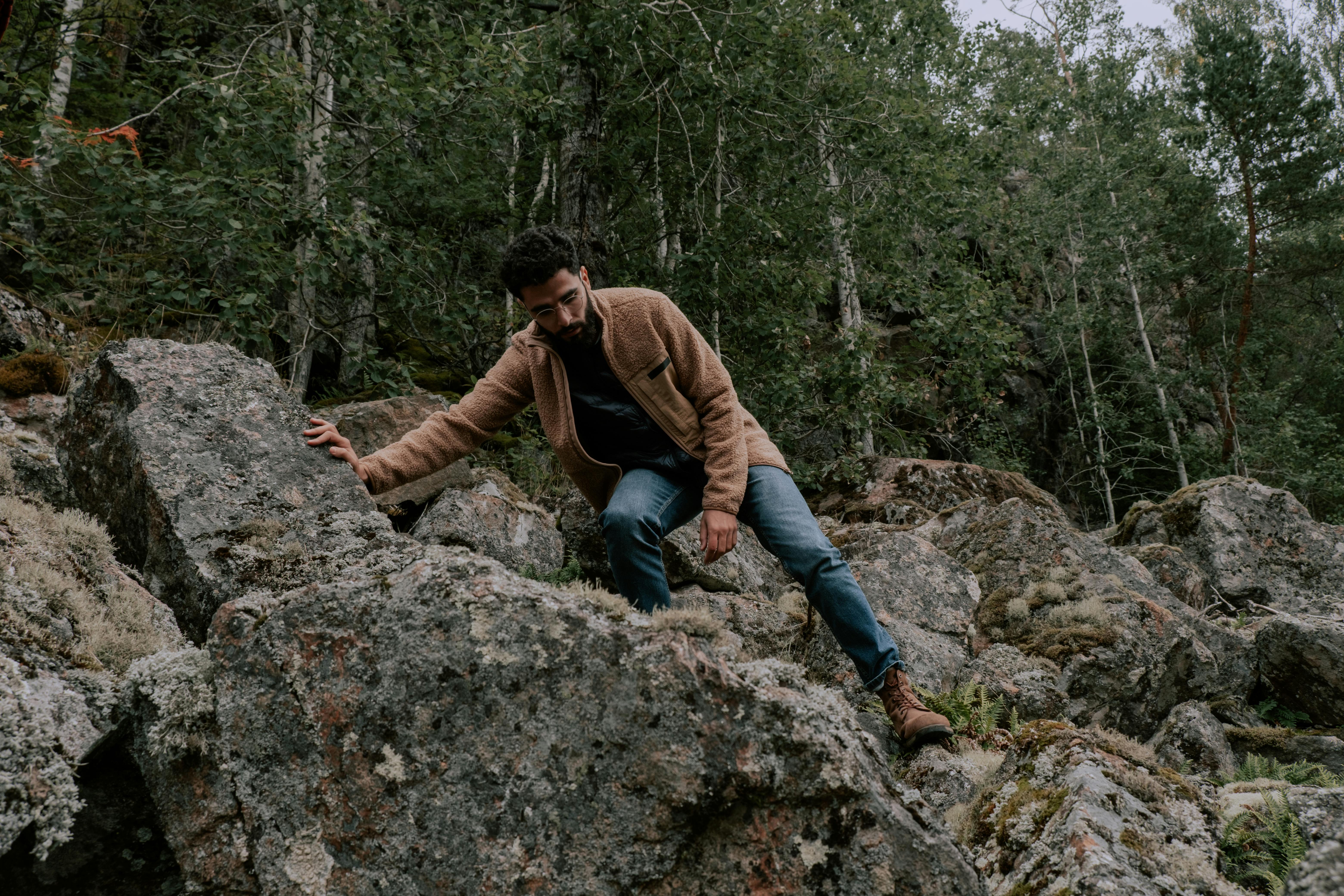 Man in Brown Jacket Walking Through Rocks Near Forest · Free Stock Photo