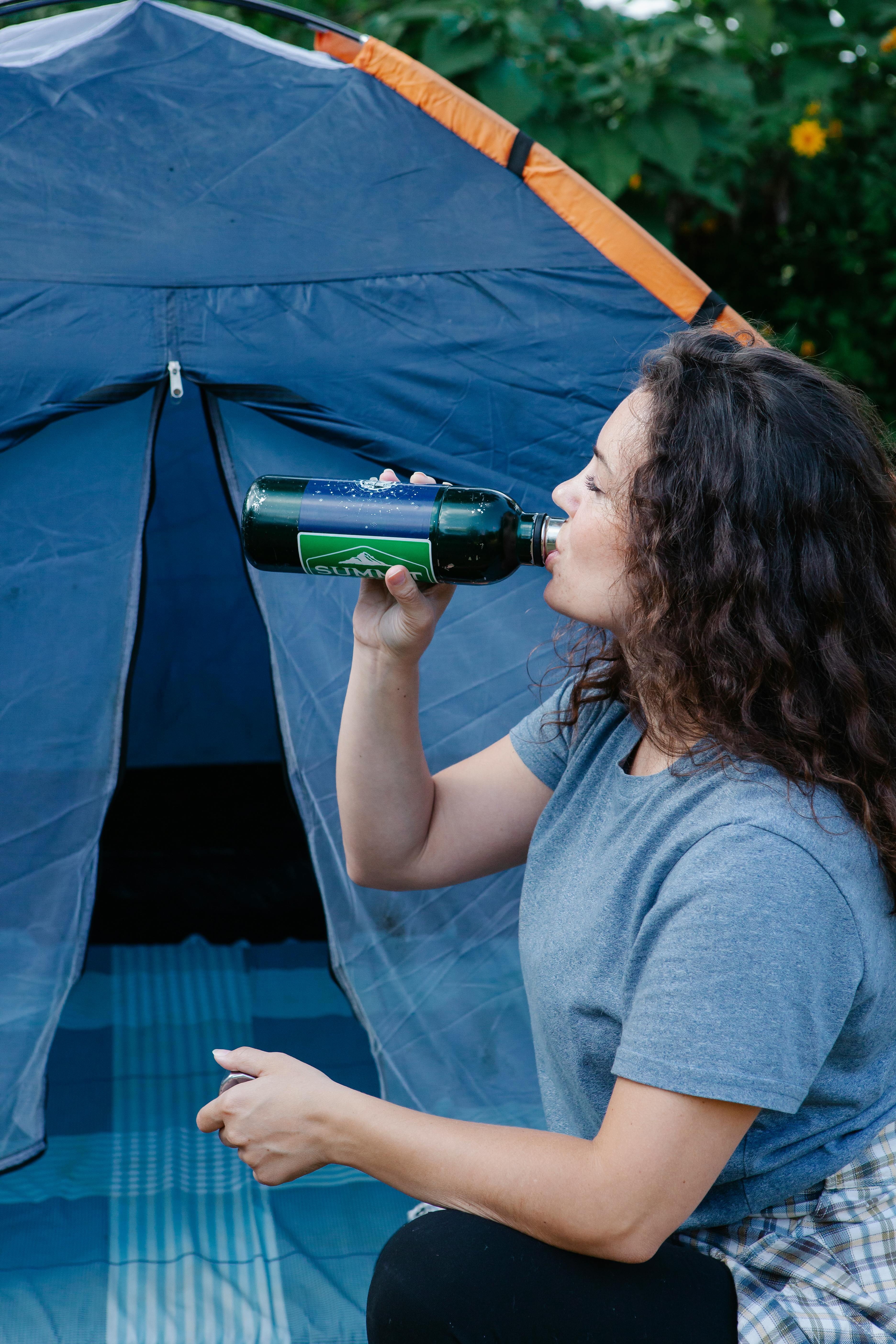 Hiker drinking beverage against tent in campsite · Free Stock Photo