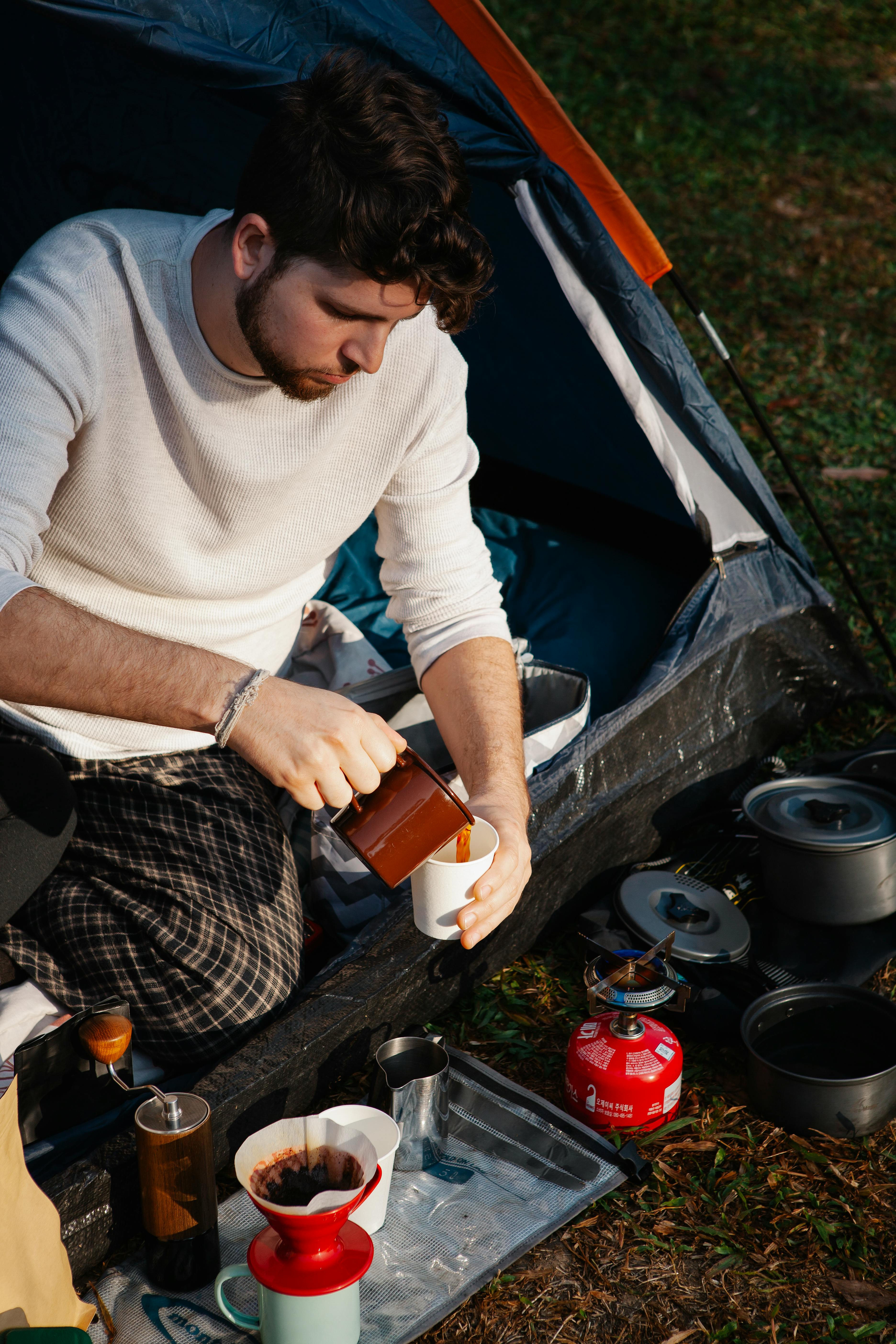Calm young man pouring coffee in camping tent · Free Stock Photo