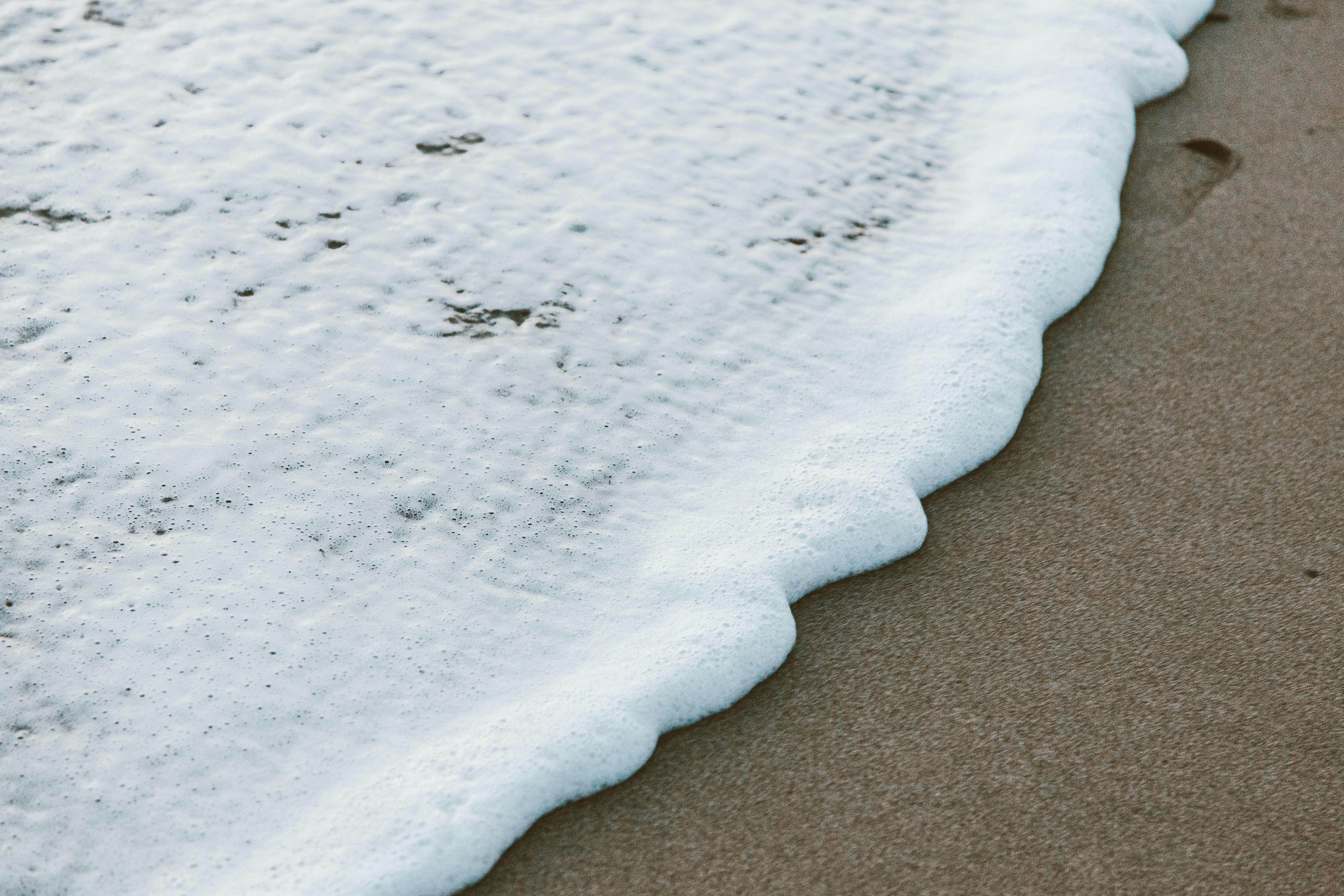 Close-Up Shot of Sea Foam on Brown Sand · Free Stock Photo