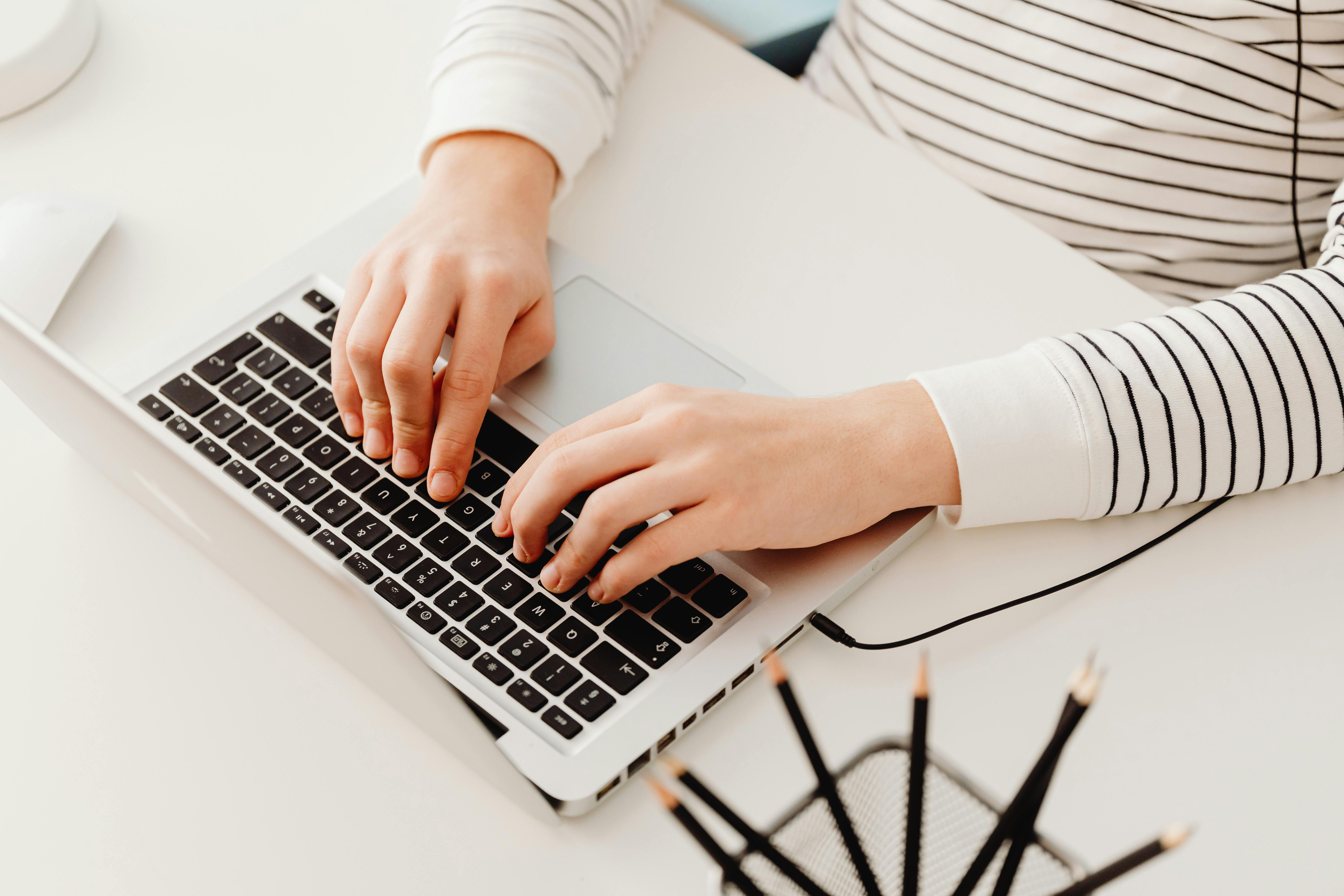 A Person Sitting at a Desk Typing on a Laptop · Free Stock Photo