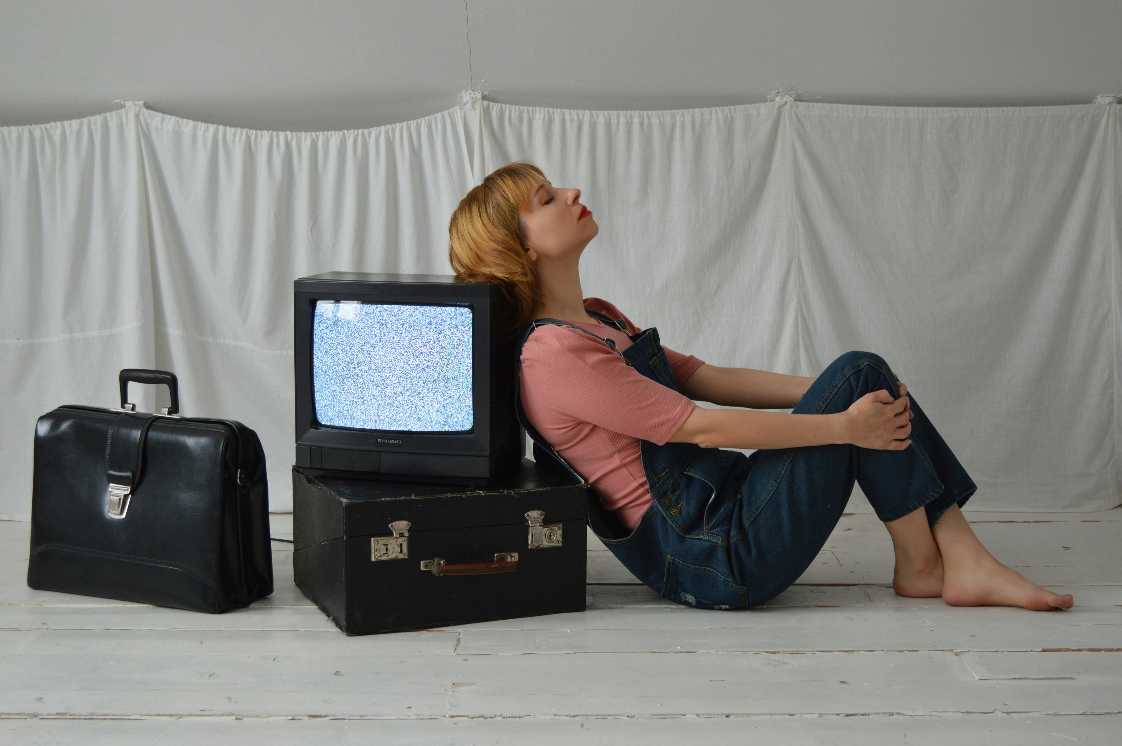 Thoughtful woman laying back on retro TV set on floor · Free Stock Photo