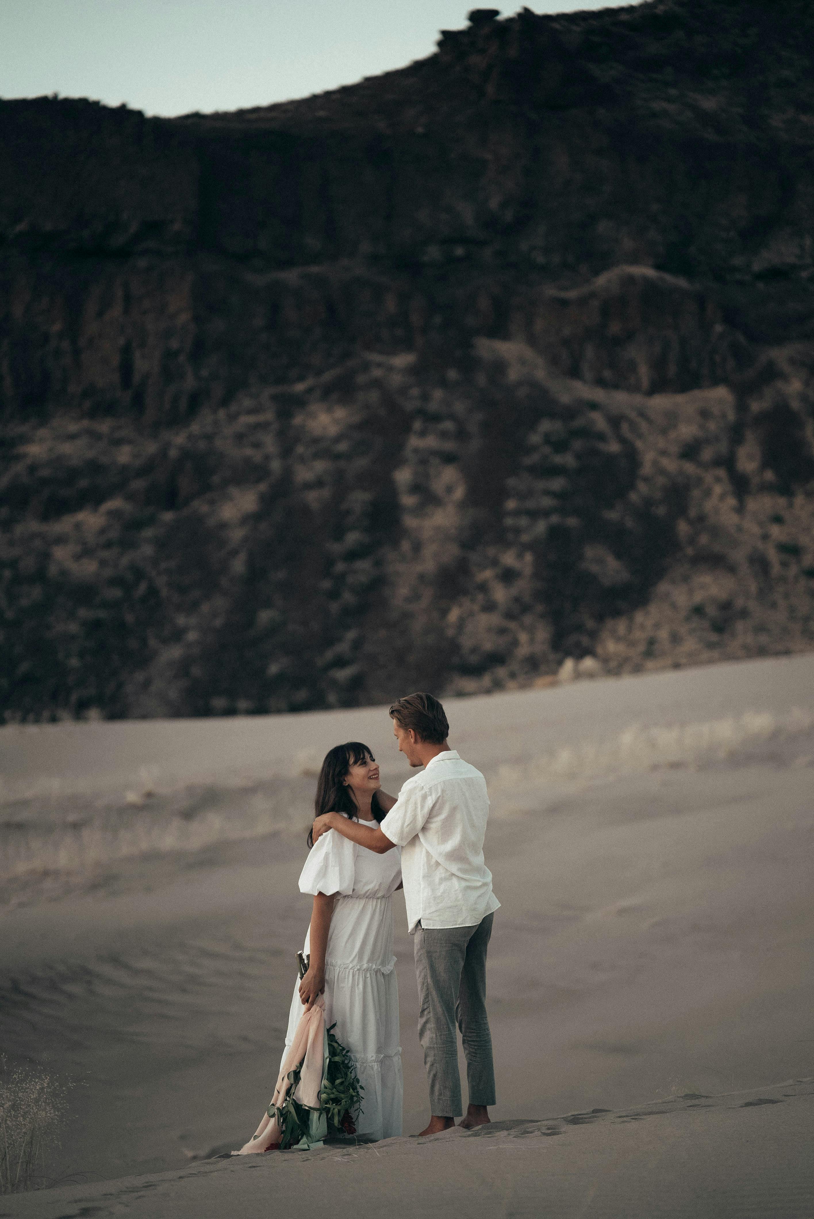 Faceless couple on sandy coast near hills · Free Stock Photo