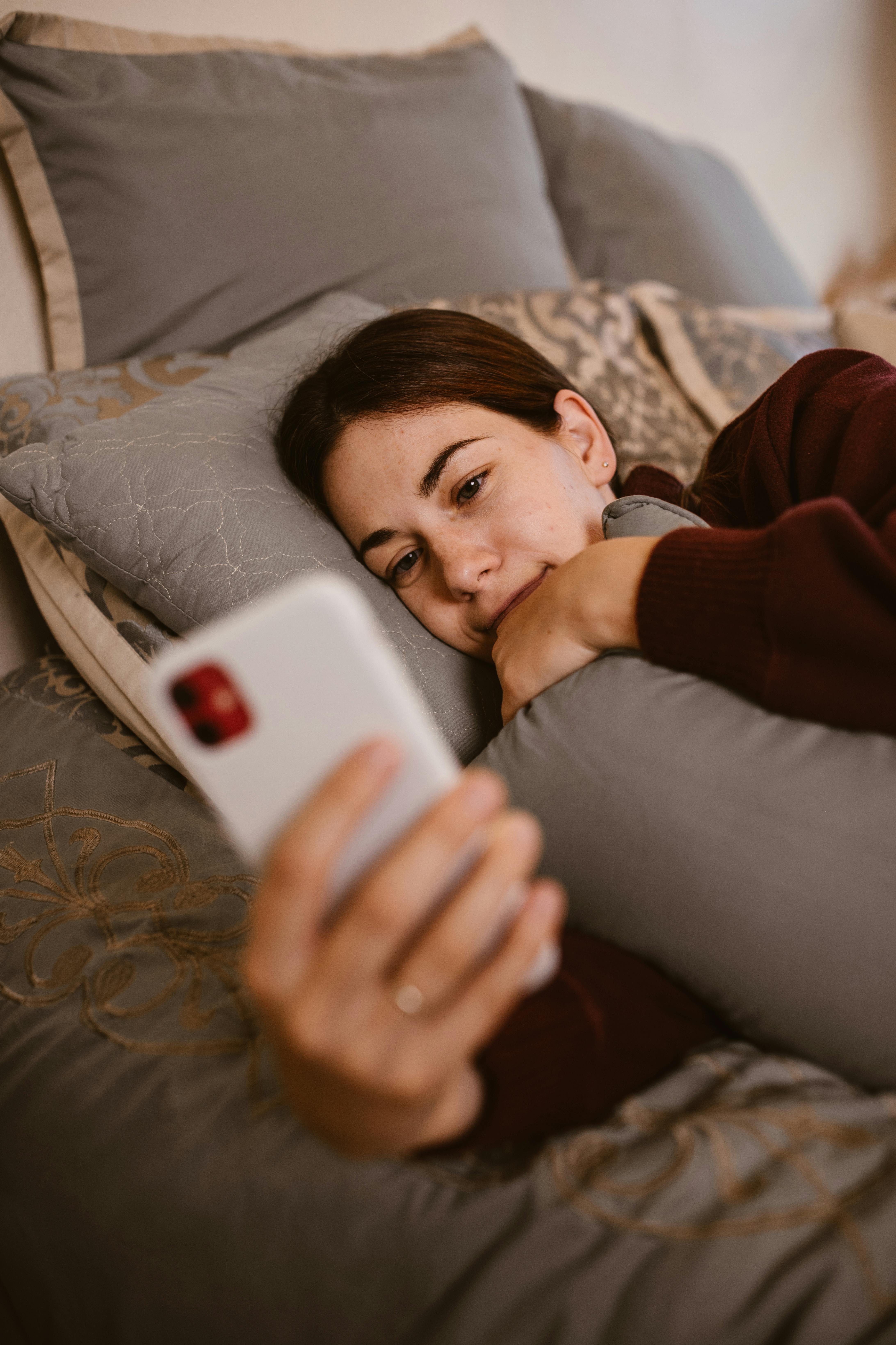 A Woman Using Her Smartphone while Lying Down in Bed · Free Stock Photo