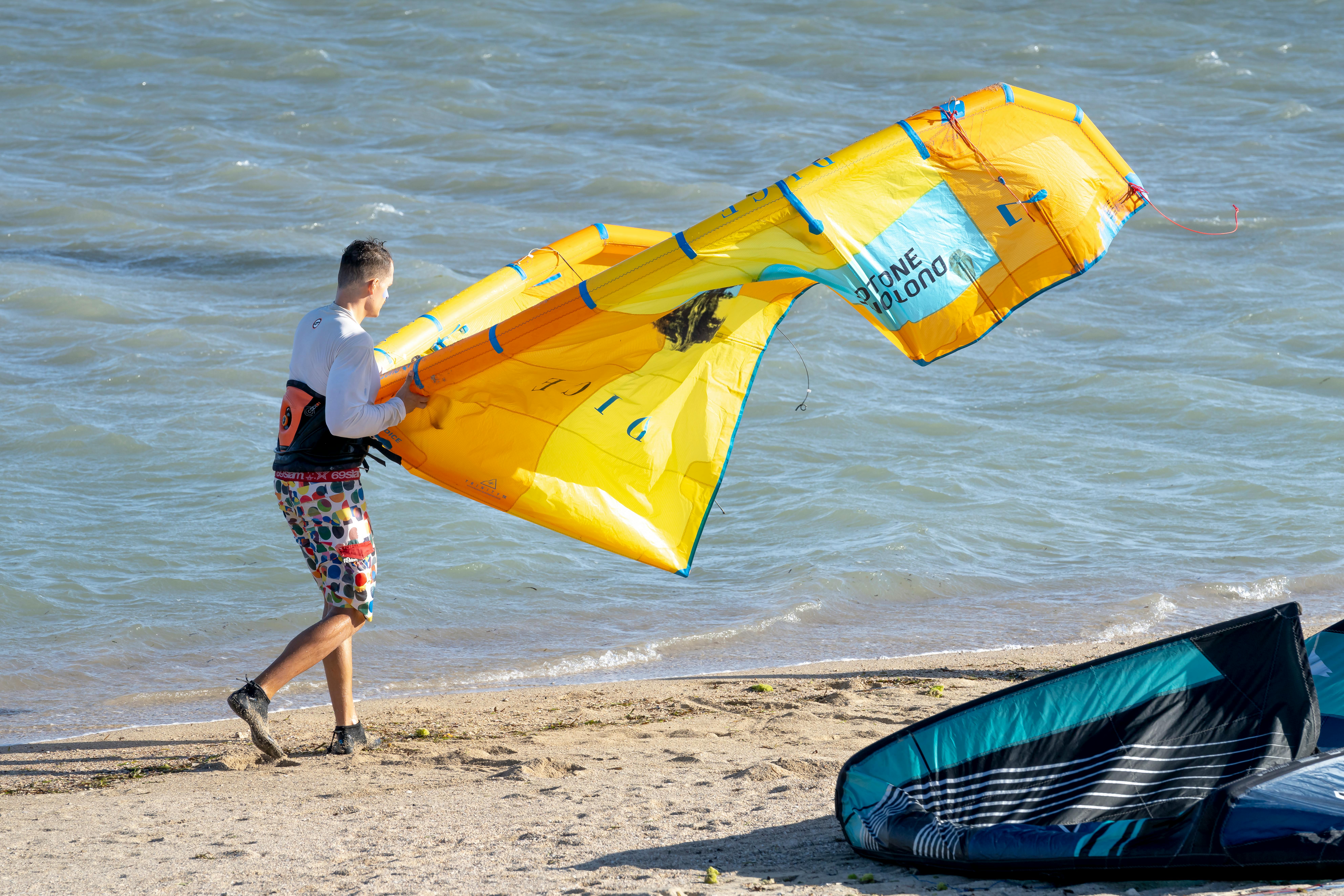 Young kitesurfer carrying kite while walking on sandy seashore · Free ...