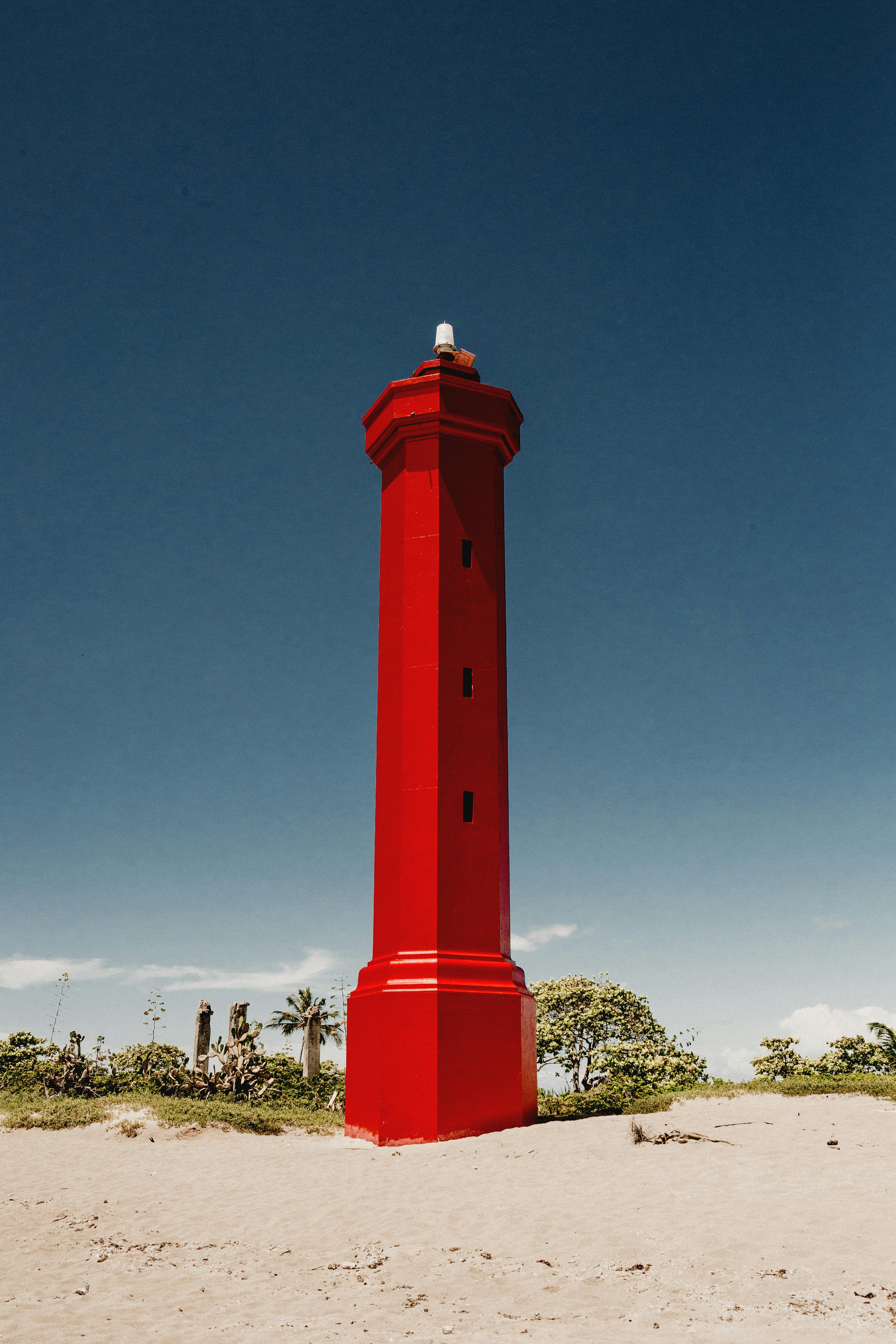 Red lighthouse placed on sandy beach in sunny day · Free Stock Photo