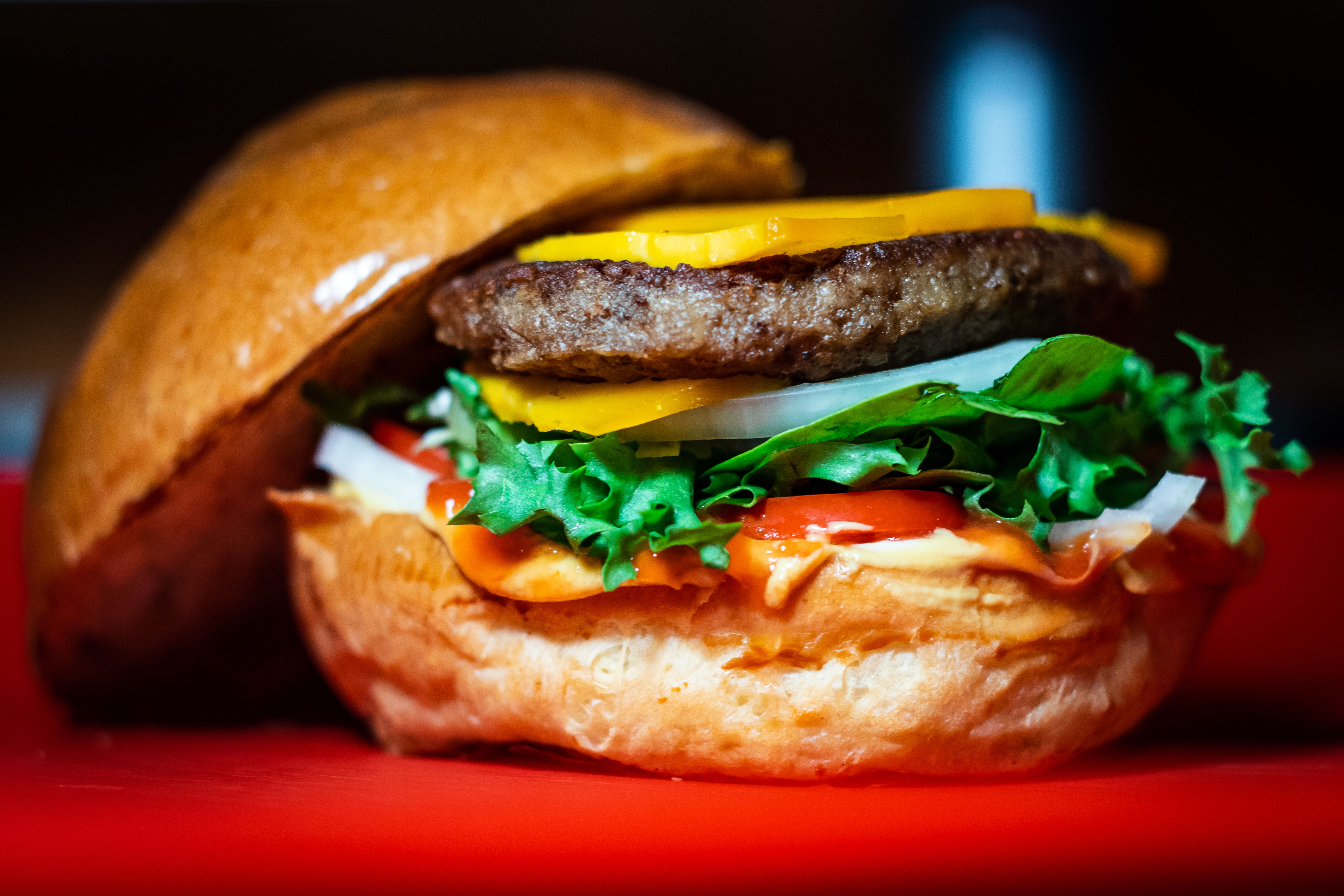Burger with Cheese and Vegetables on Red Surface · Free Stock Photo