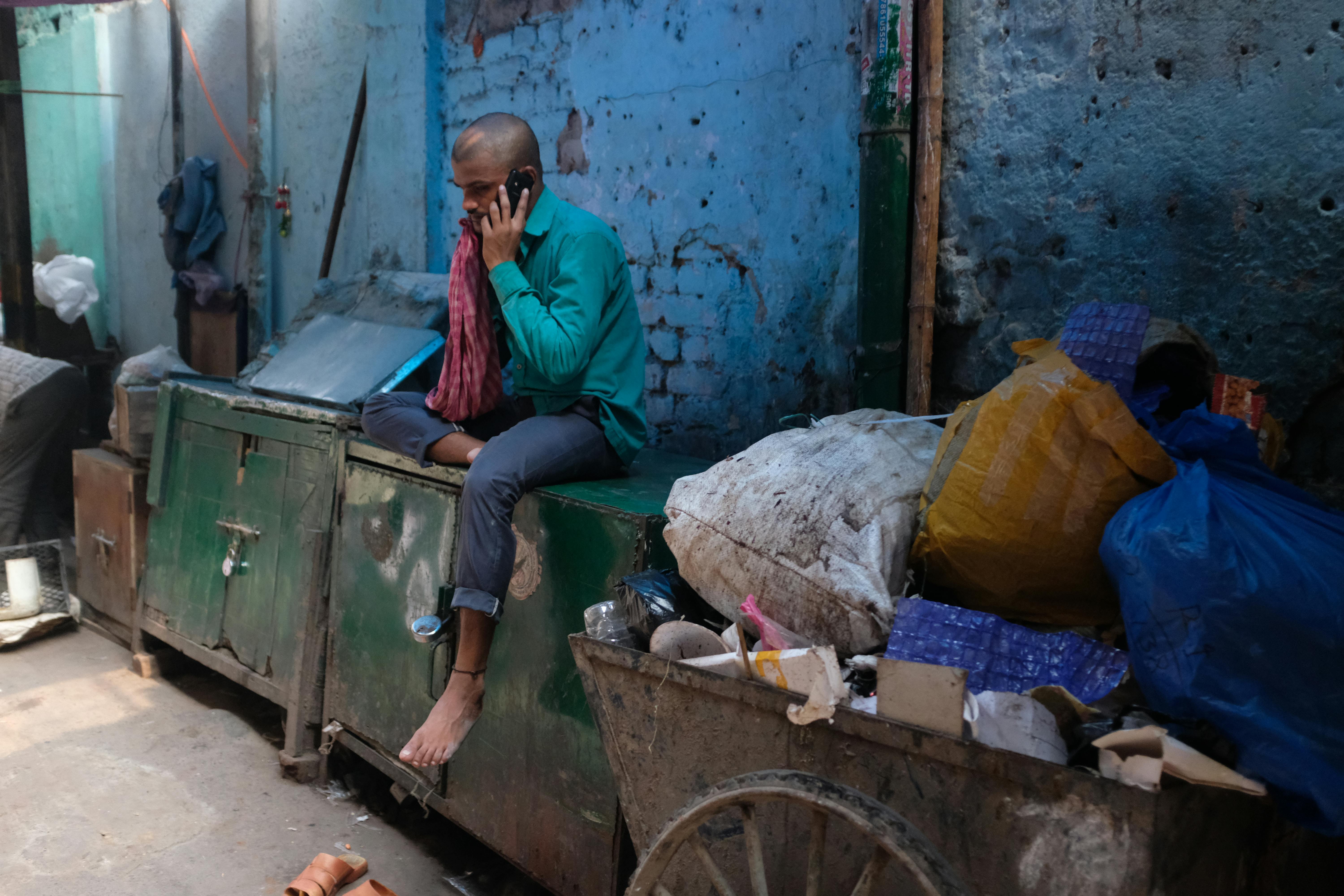 Man Sitting and Talking on Cellphone Near Garbage Dump · Free Stock Photo