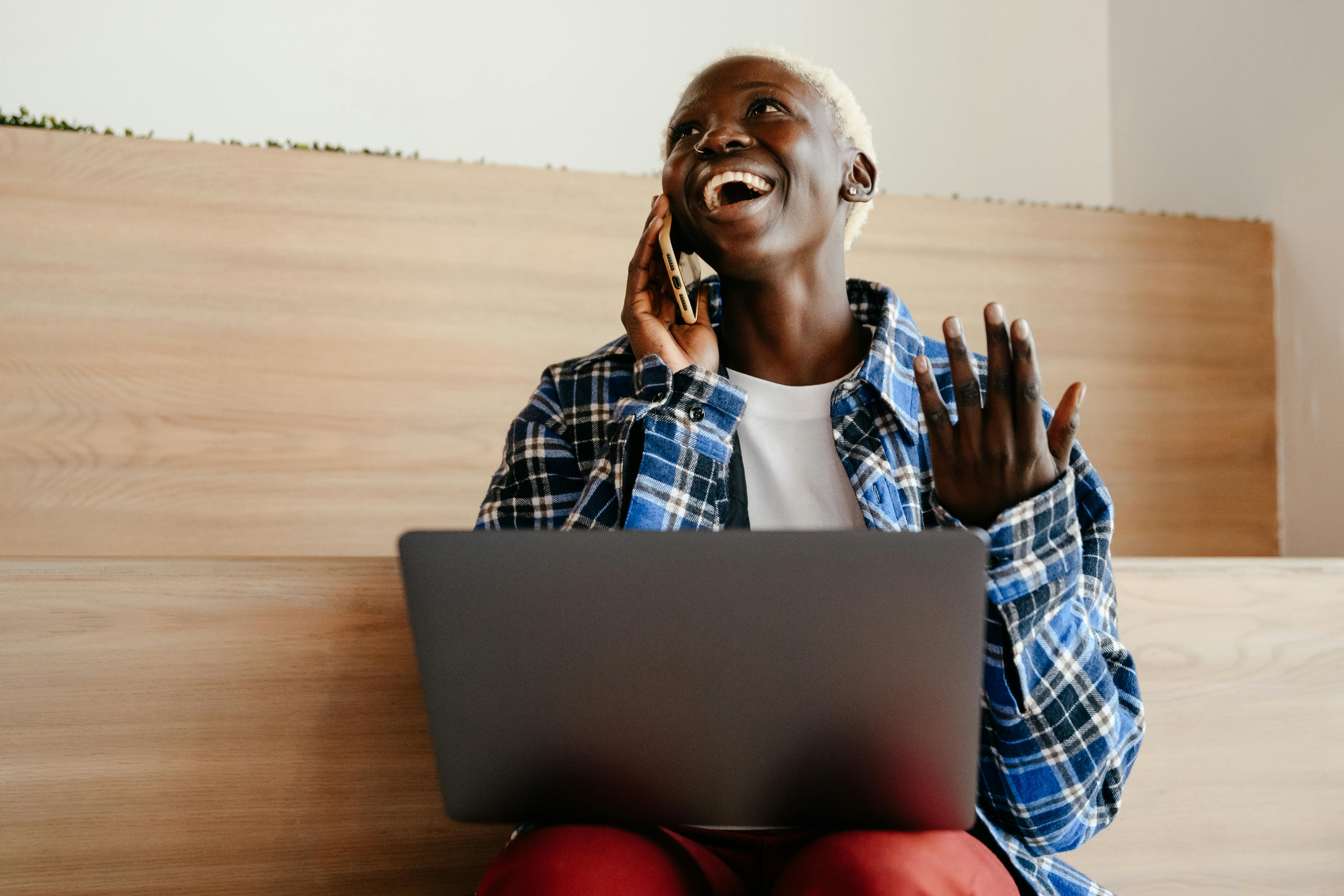 Cheerful black woman with laptop talking on smartphone and smiling ...
