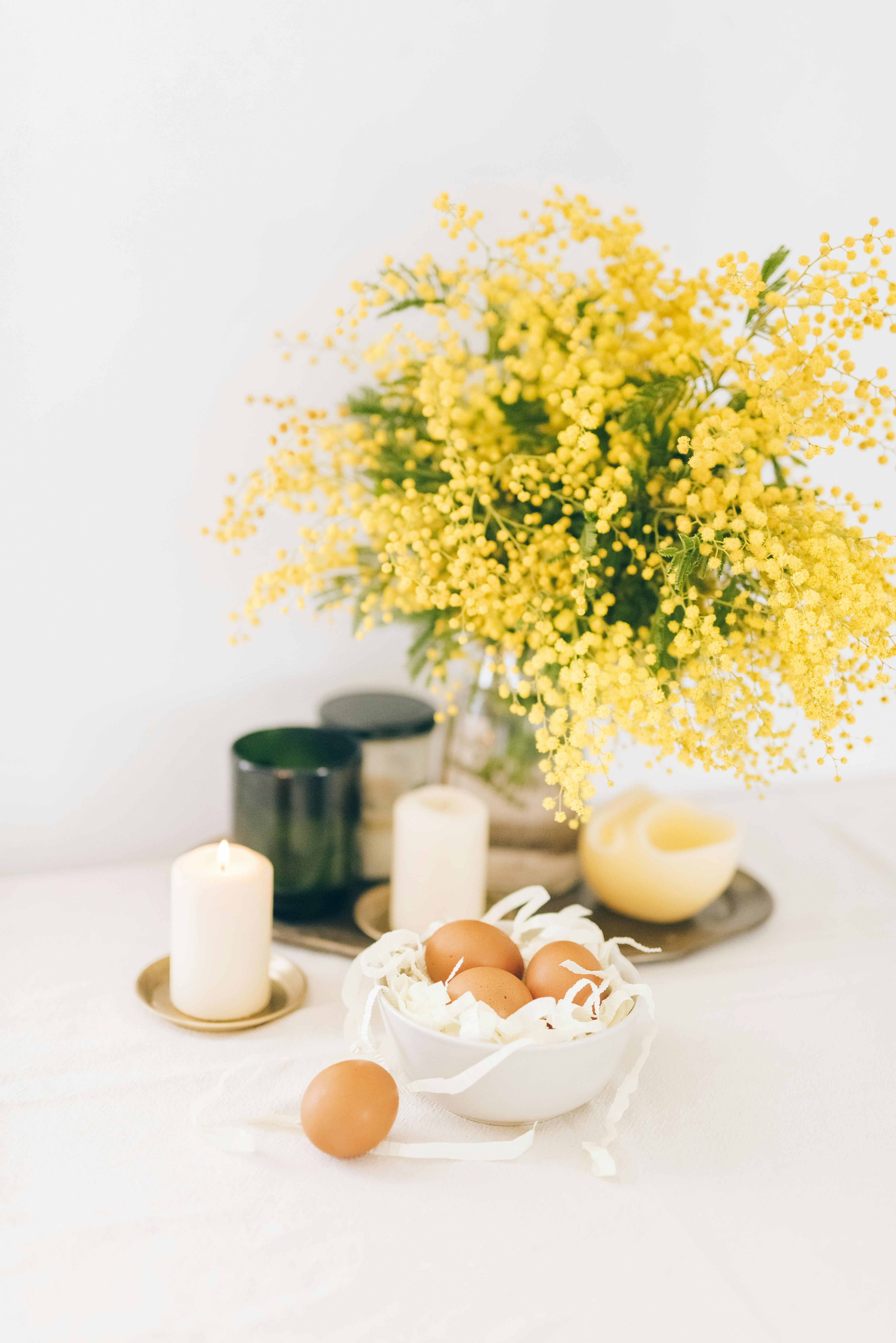 Yellow Flowers And Lighted Candles Beside A Bowl Of Brown Eggs On Table ...