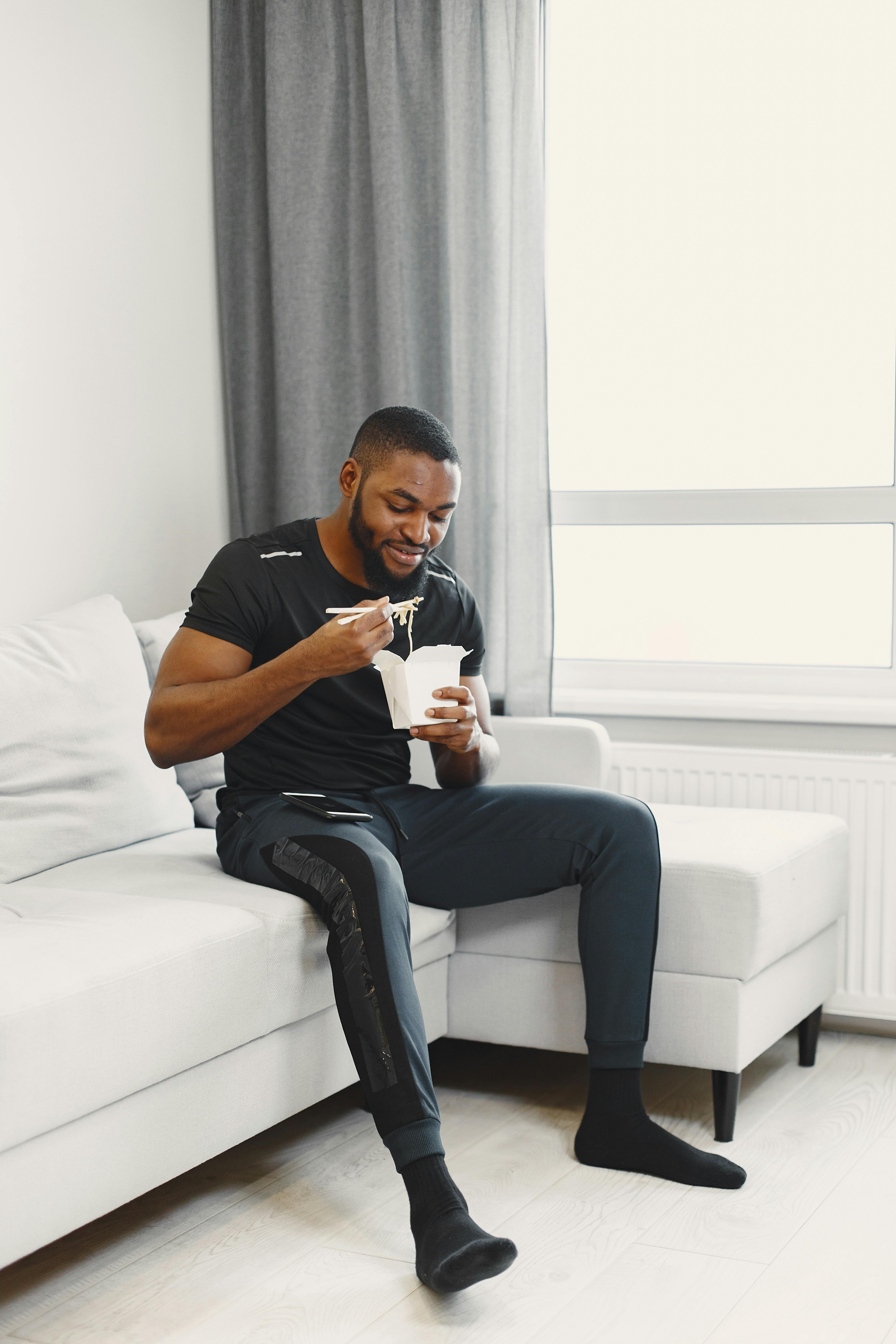 Man Sitting on Sofa While Eating · Free Stock Photo