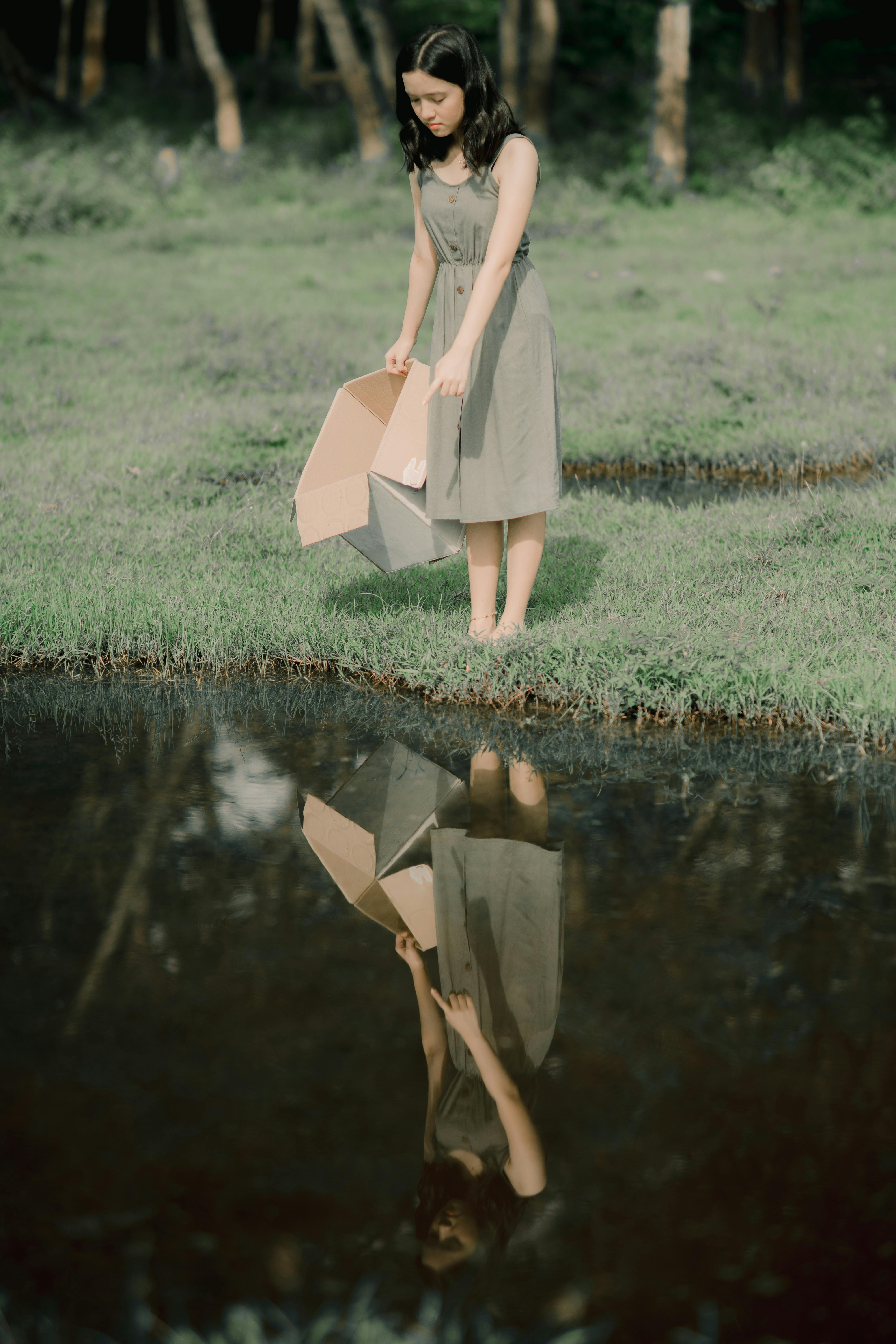 Crop woman with cardboard box on meadow reflecting in water · Free ...