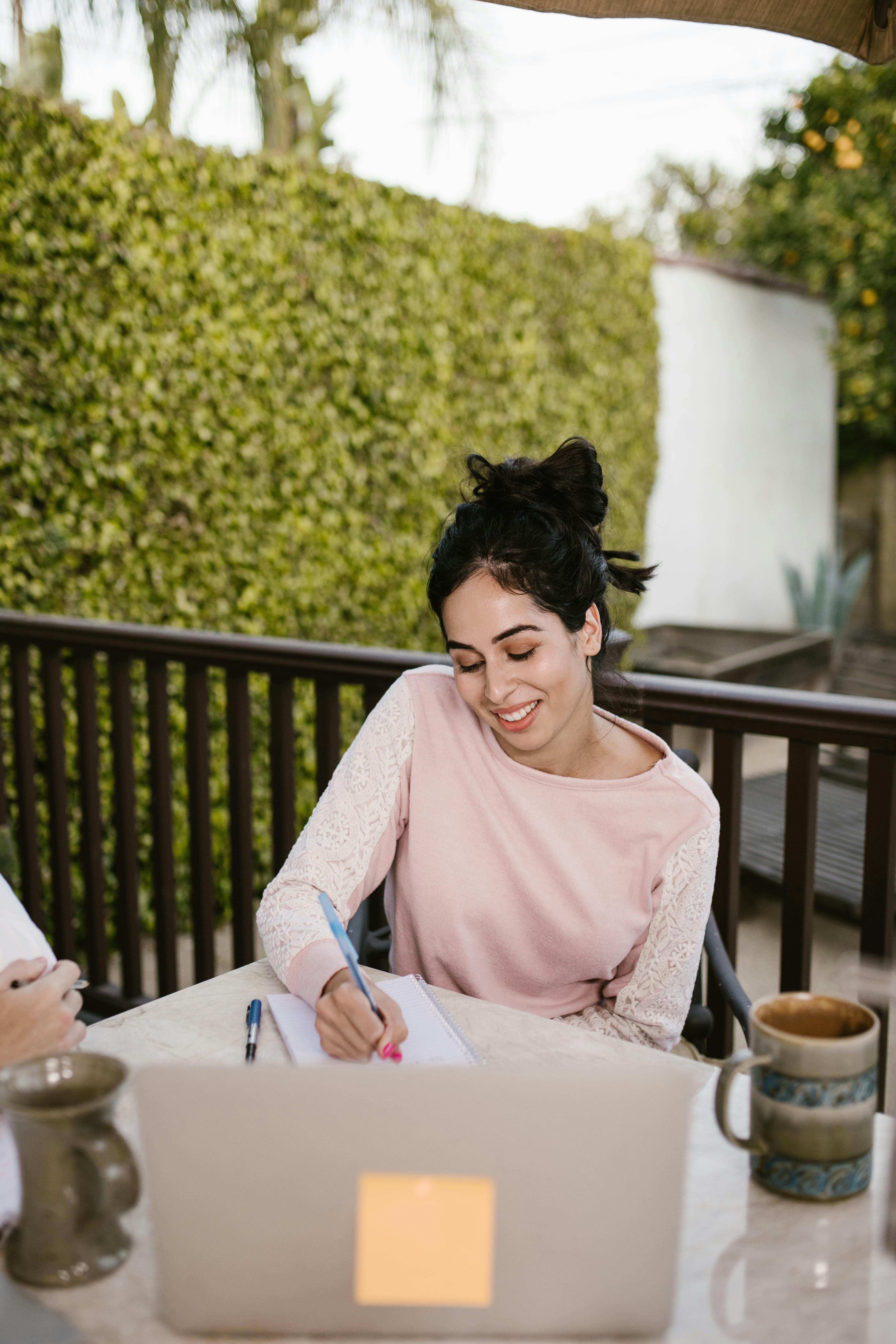 Woman Smiling While Writing on Her Notebook · Free Stock Photo