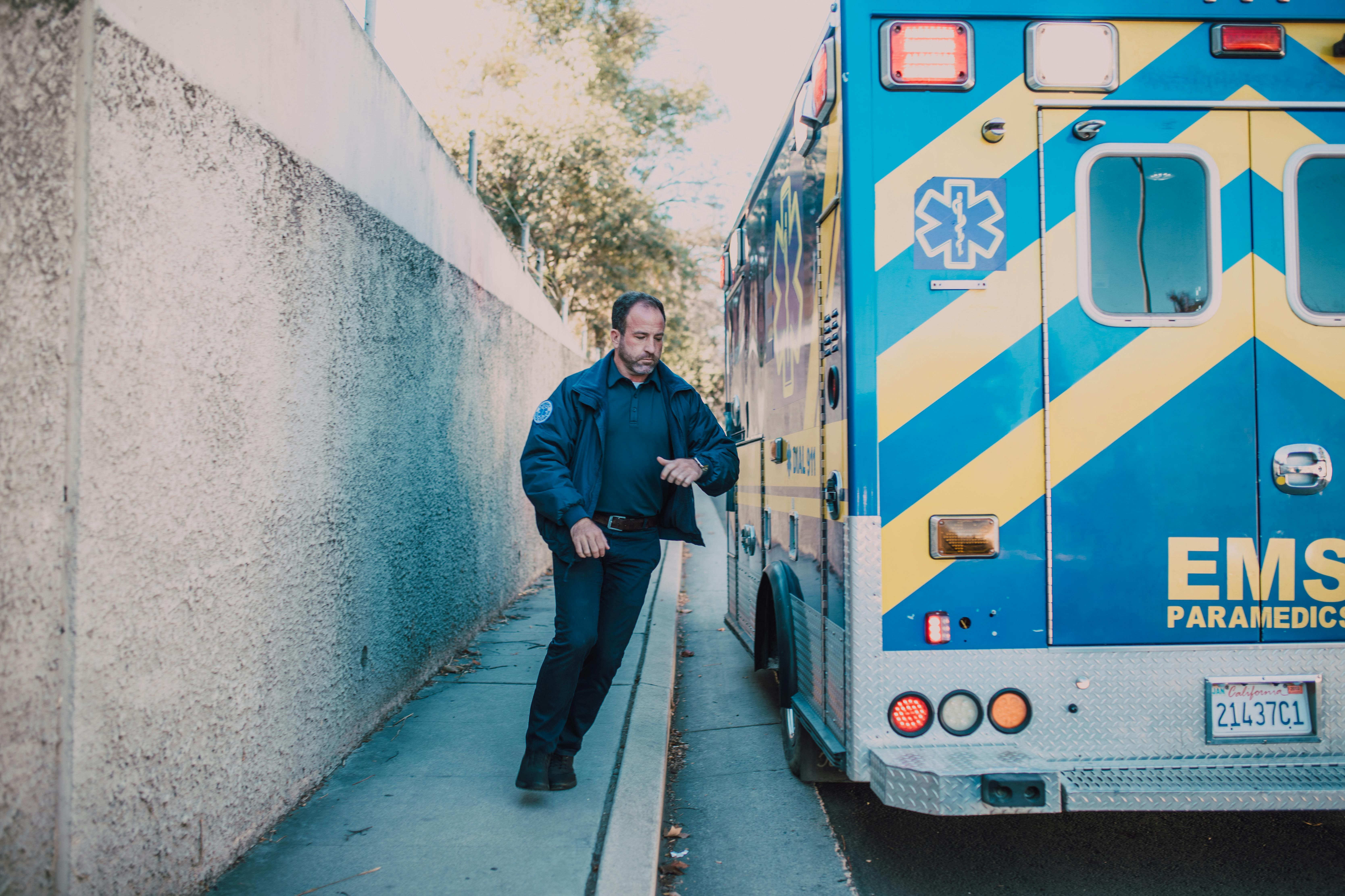 Man in Blue Jacket Standing Walking Beside an Ambulance · Free Stock Photo