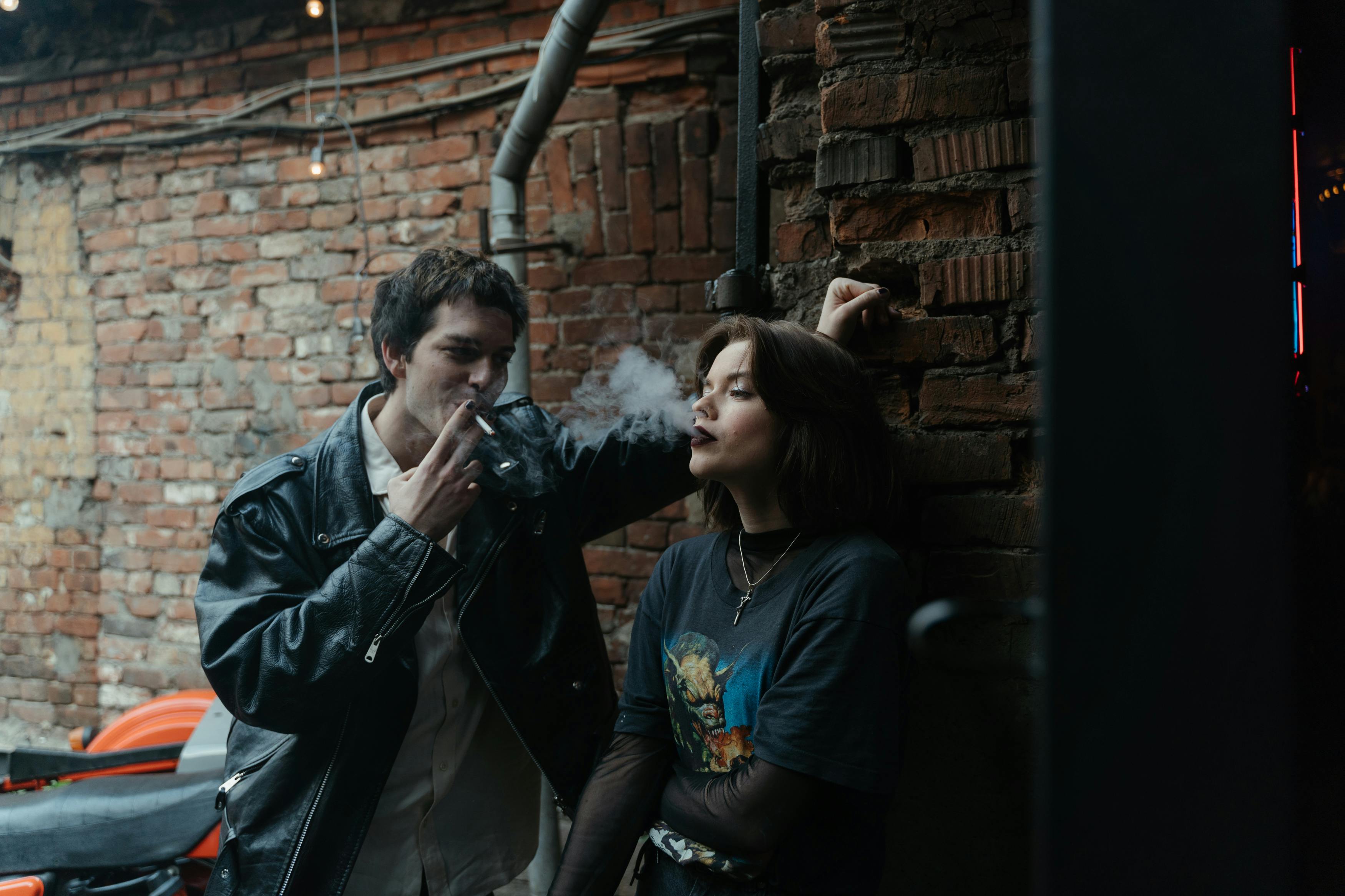 Man and Woman Smoking Together Near Brick Wall · Free Stock Photo