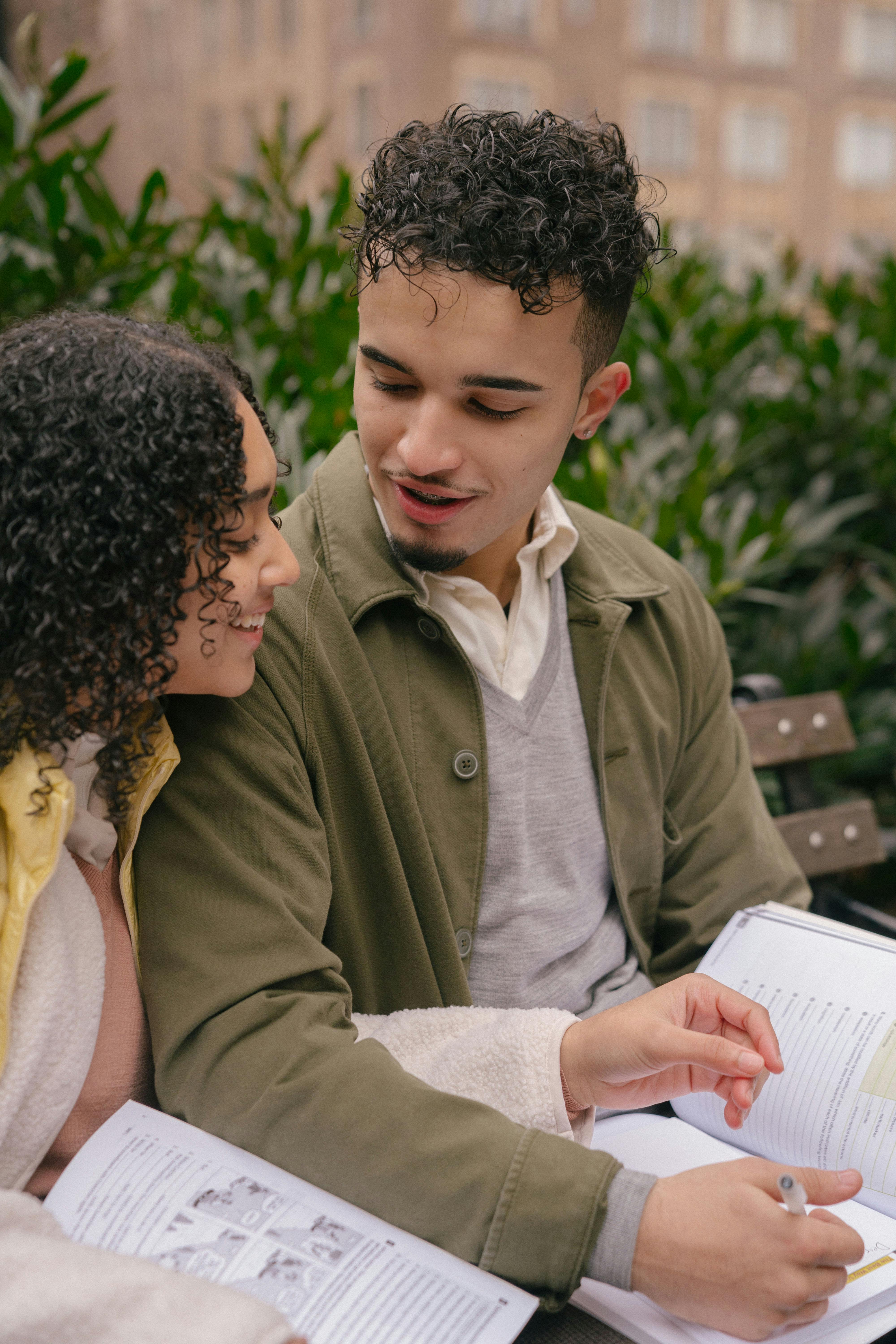 Focused couple writing in workbooks on bench in park · Free Stock Photo