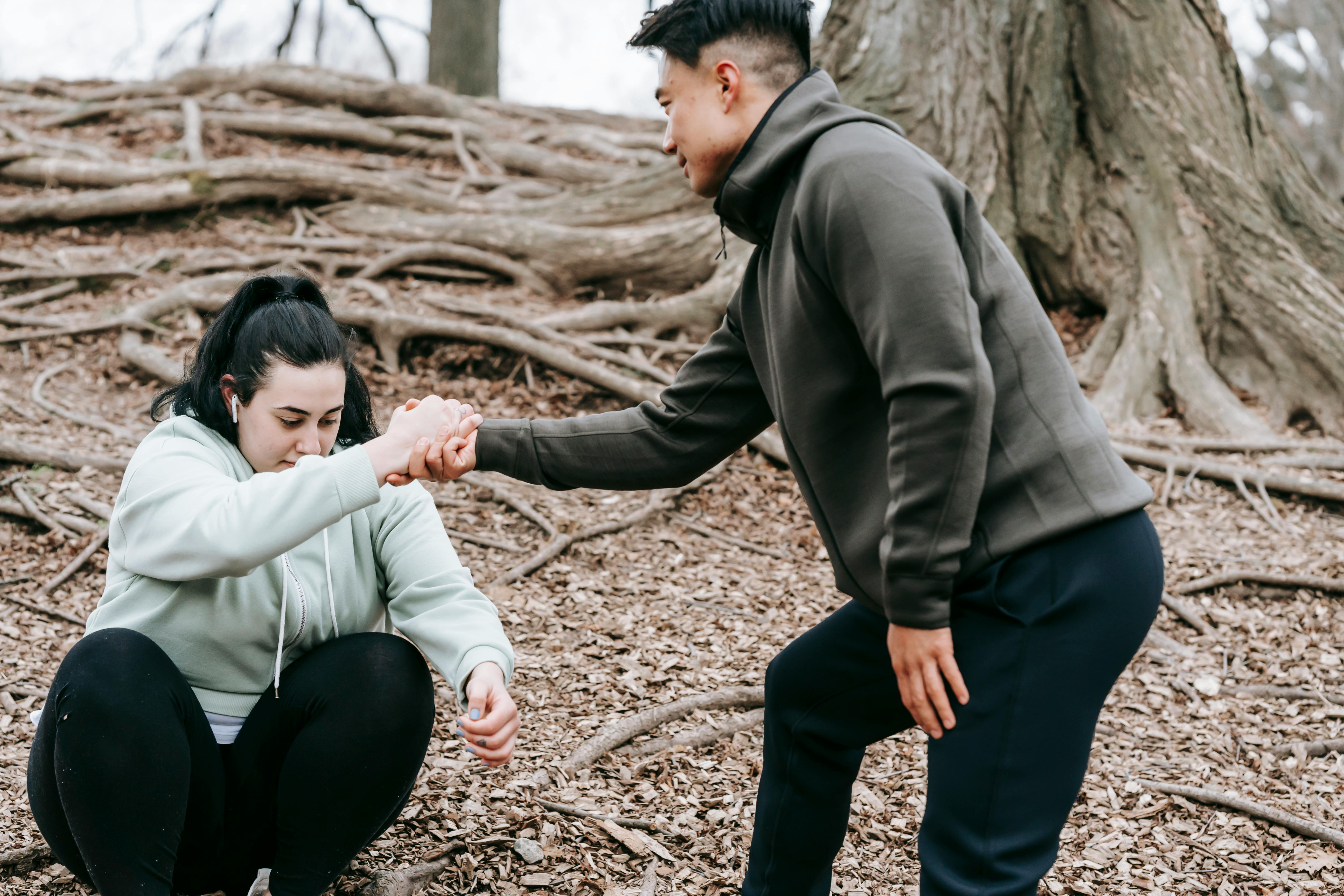 Man helping plus sized woman get up from ground in park · Free Stock Photo