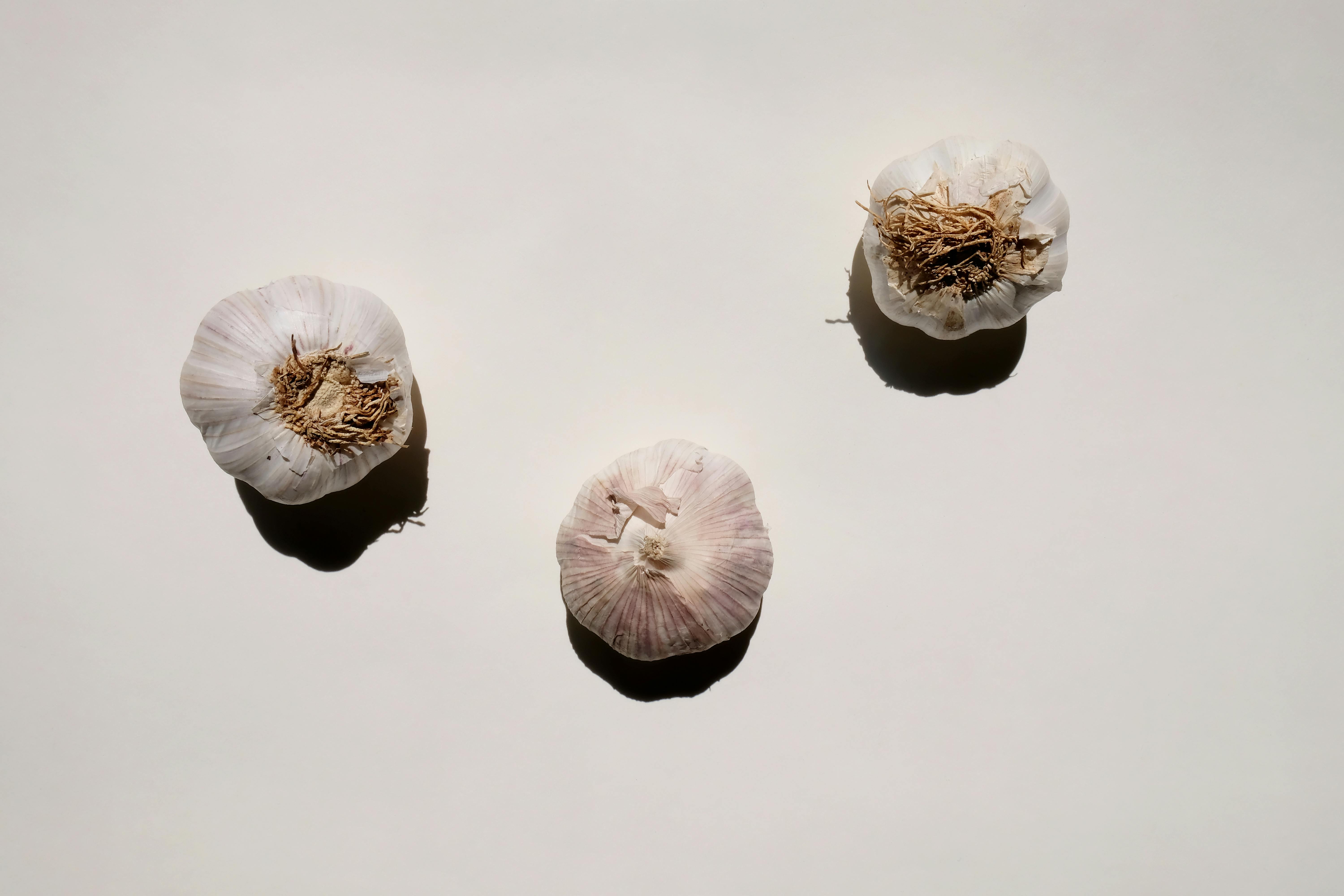 Close-Up Photo of Three Garlic on Wooden Surface · Free Stock Photo