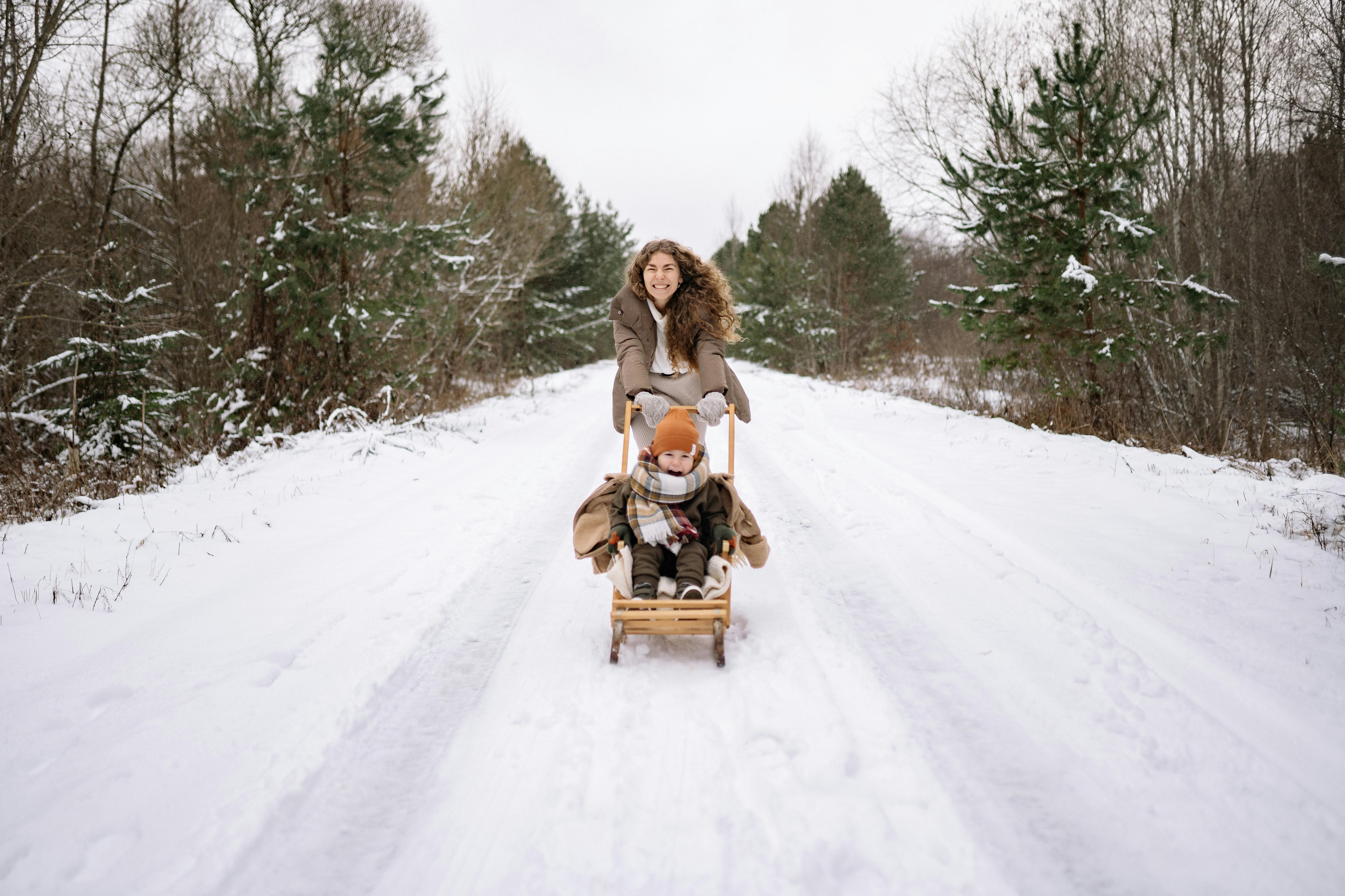 A Woman Pushing a Boy on a Sledge on Snow Covered Ground · Free Stock Photo