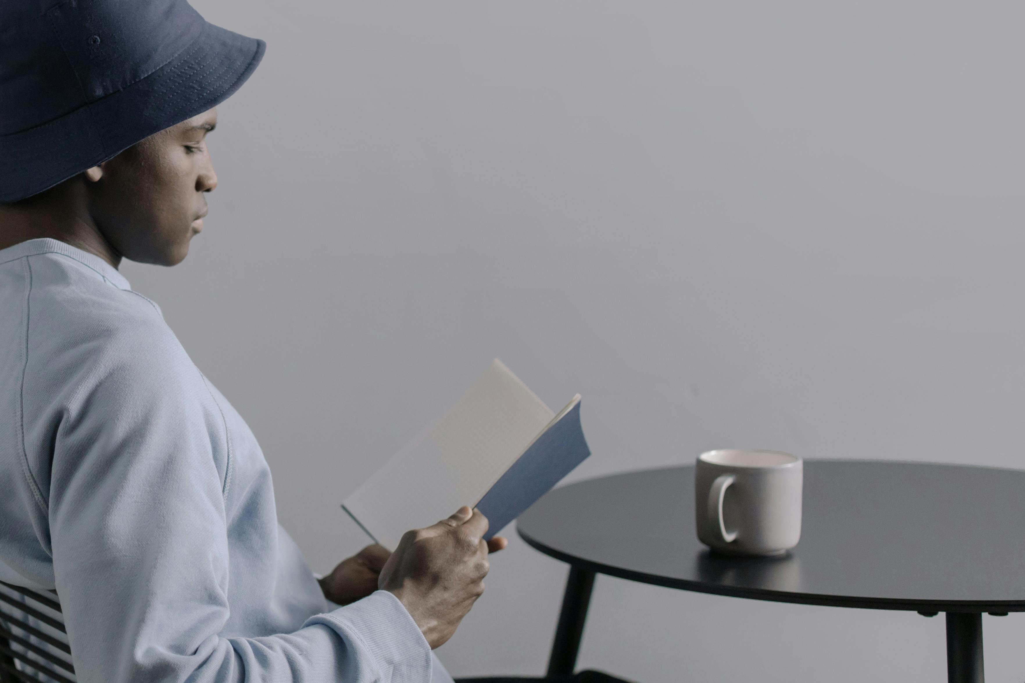 Man in Long Sleeve Shirt and Bucket Hat Covering His Face With a Book ...
