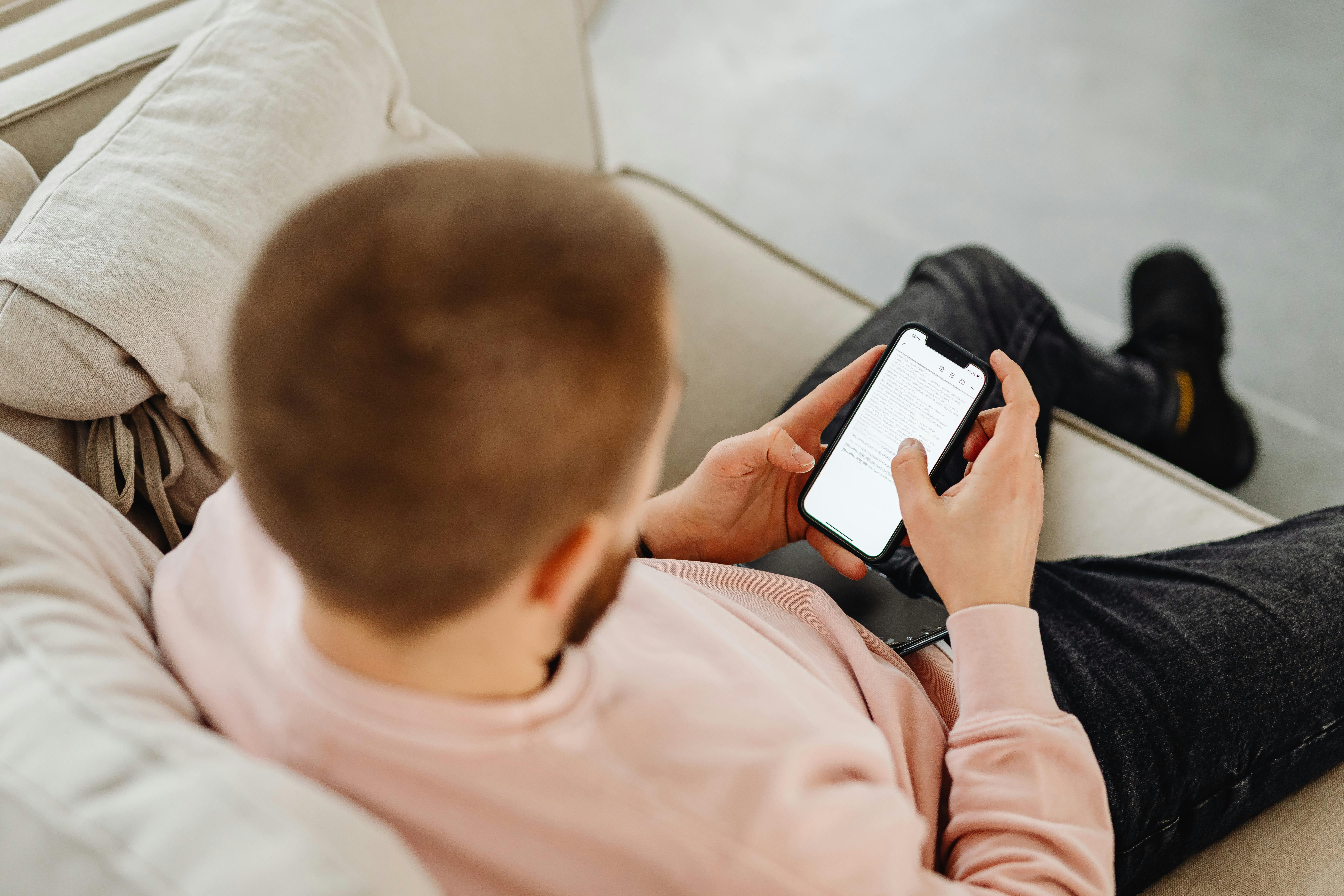 A Man Sitting on Sofa Holding Black Smartphone · Free Stock Photo