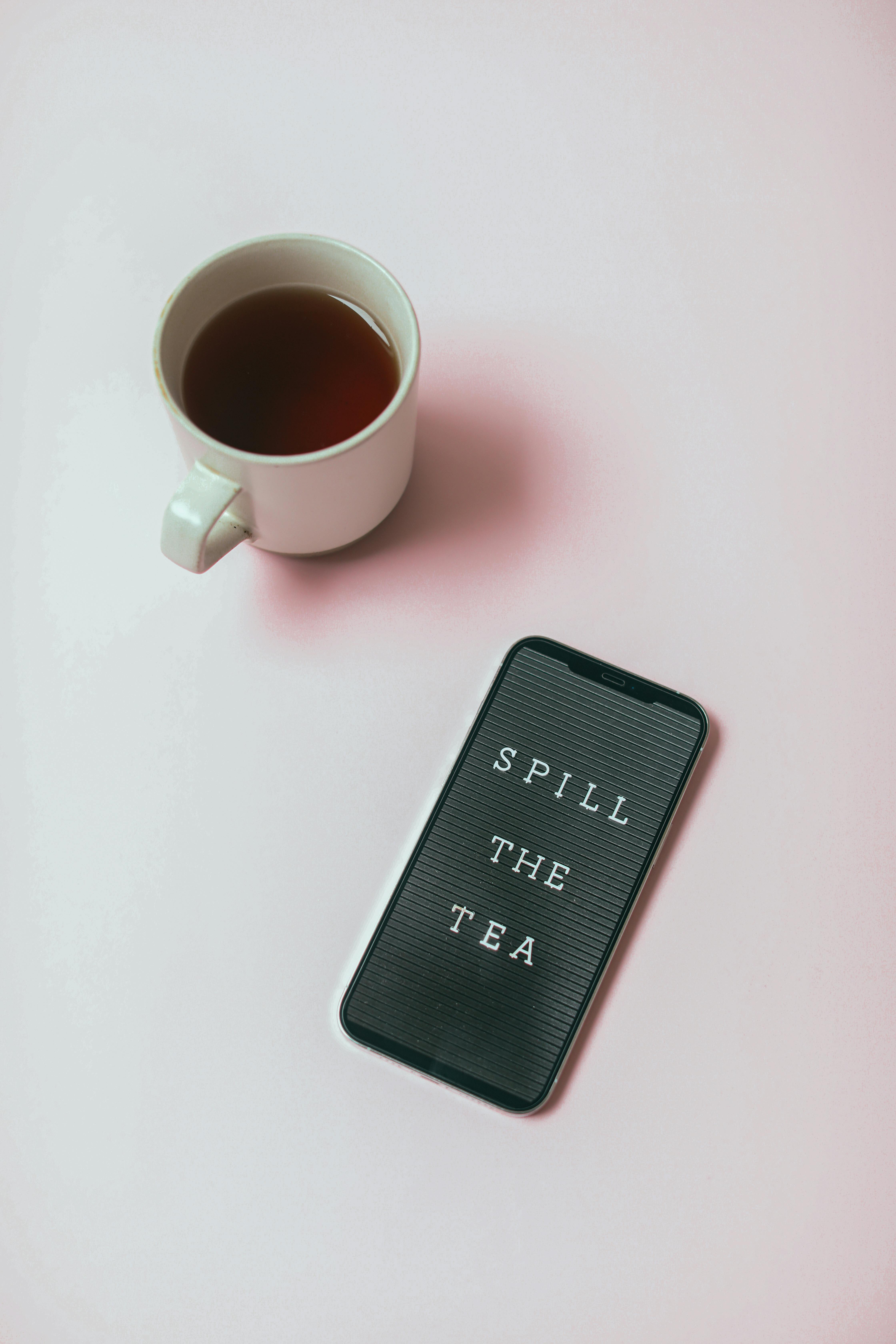 A Cellphone Beside a Cup of Tea on a White Surface · Free Stock Photo