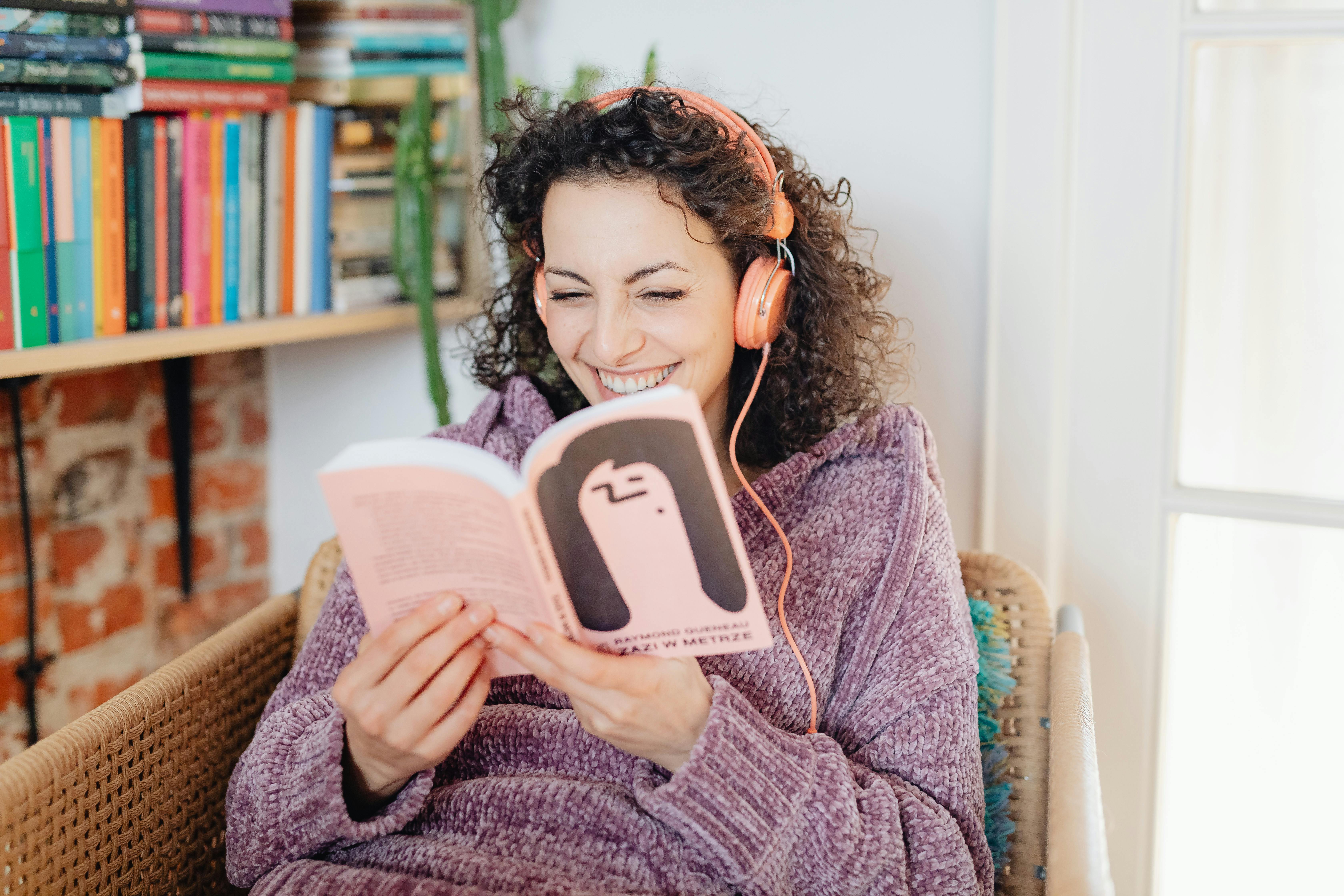 Portrait of a Smiling Woman Wearing Headphones and Reading a Book ...