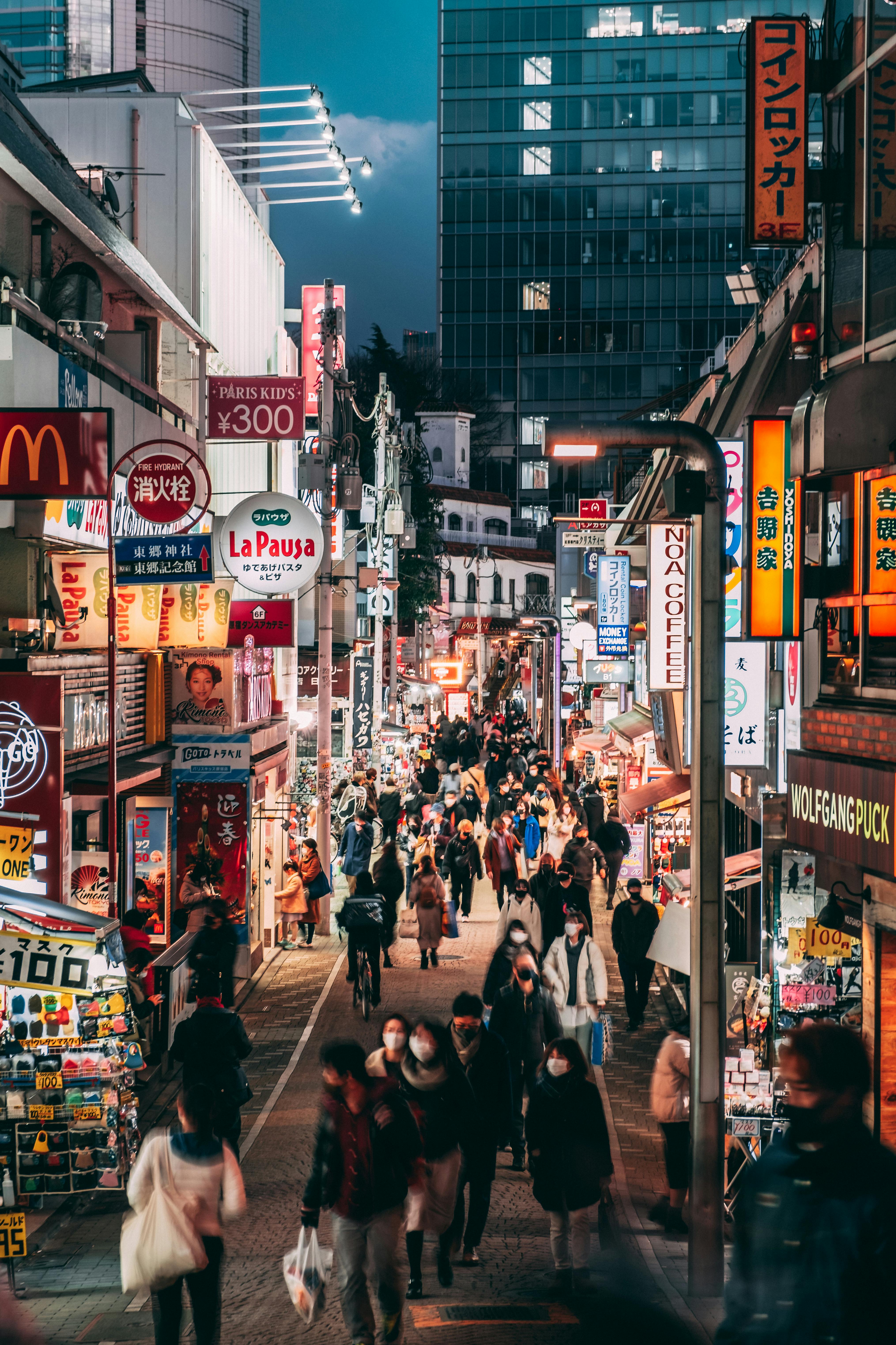 Crowded illuminated street with shops and colorful banners at night ...