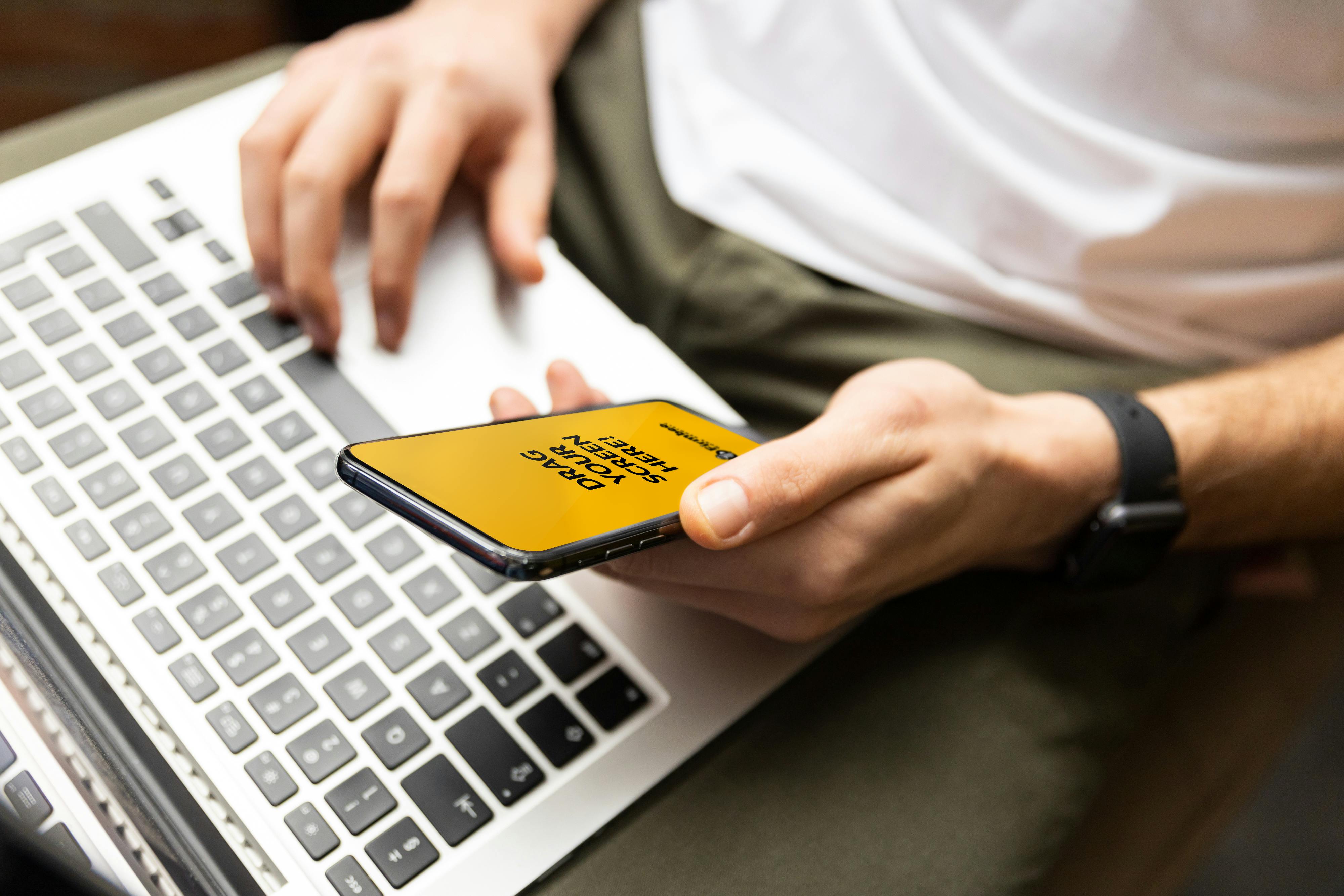 Man Holding A Smartphone While Using Laptop · Free Stock Photo