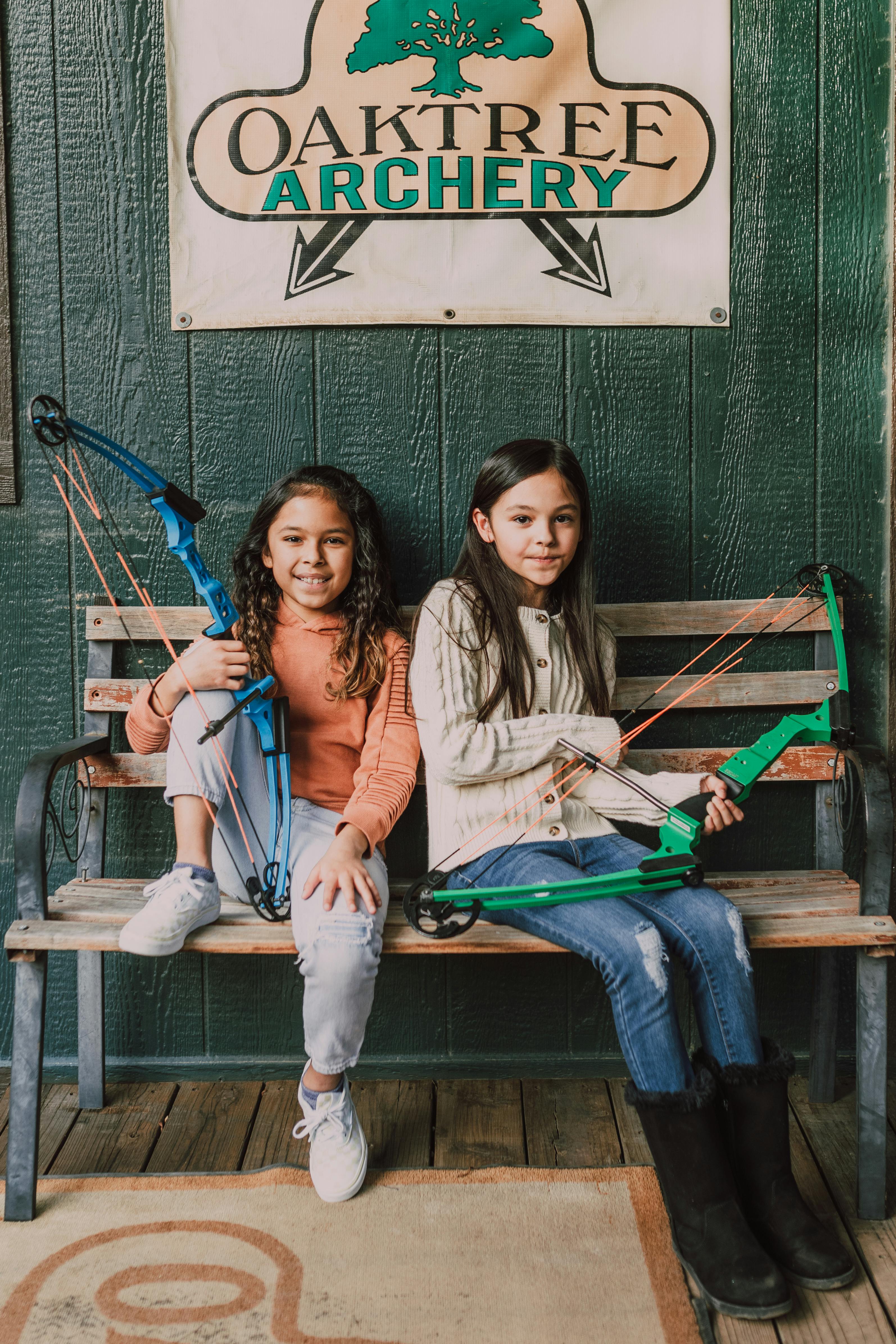 Two Girls Holding an Archery Bow while Sitting on a Wooden Bench · Free ...