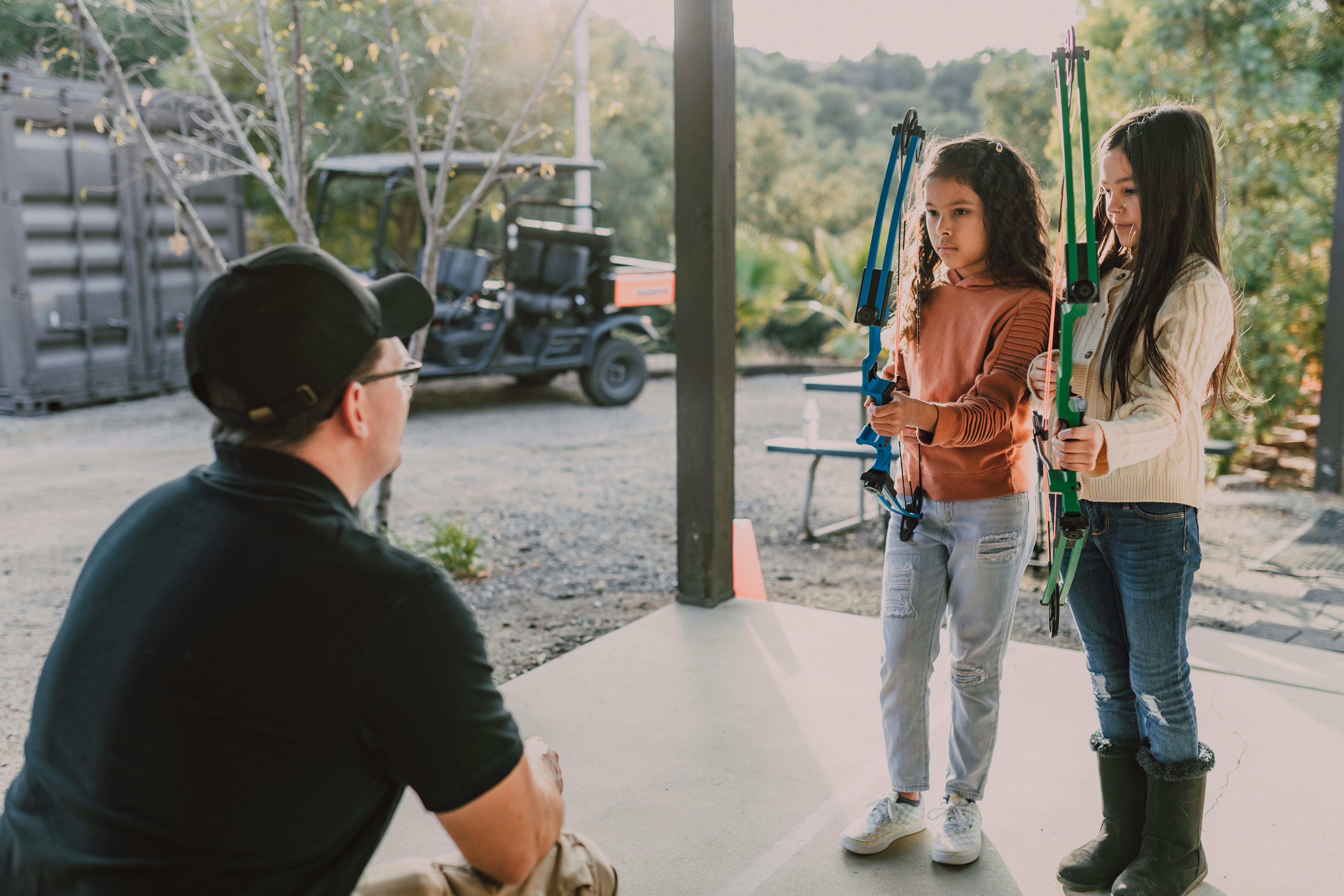 A Man Teaching Two Girls How To Use A Bow · Free Stock Photo