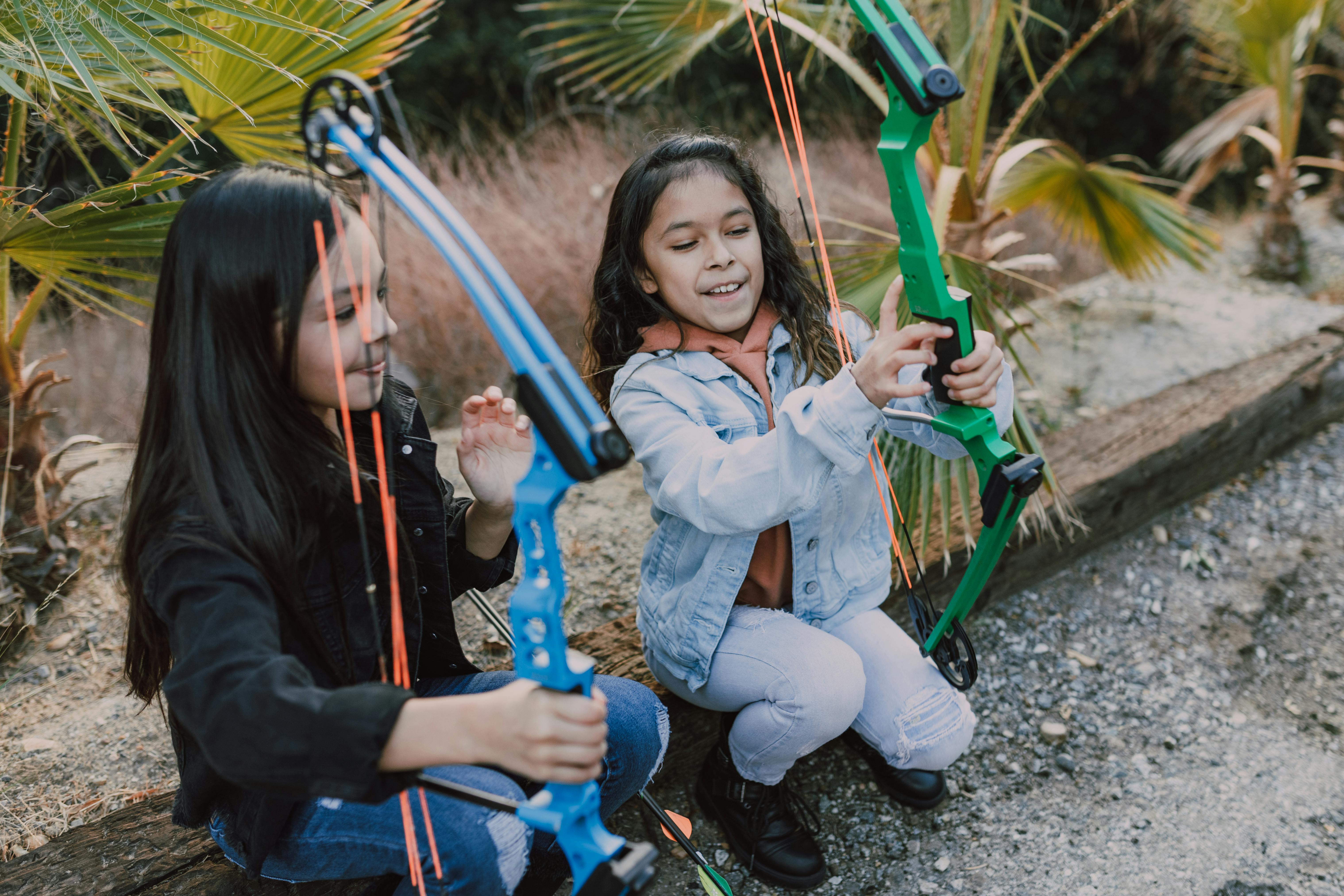 Two Girls Holding an Archery Bow while Sitting · Free Stock Photo
