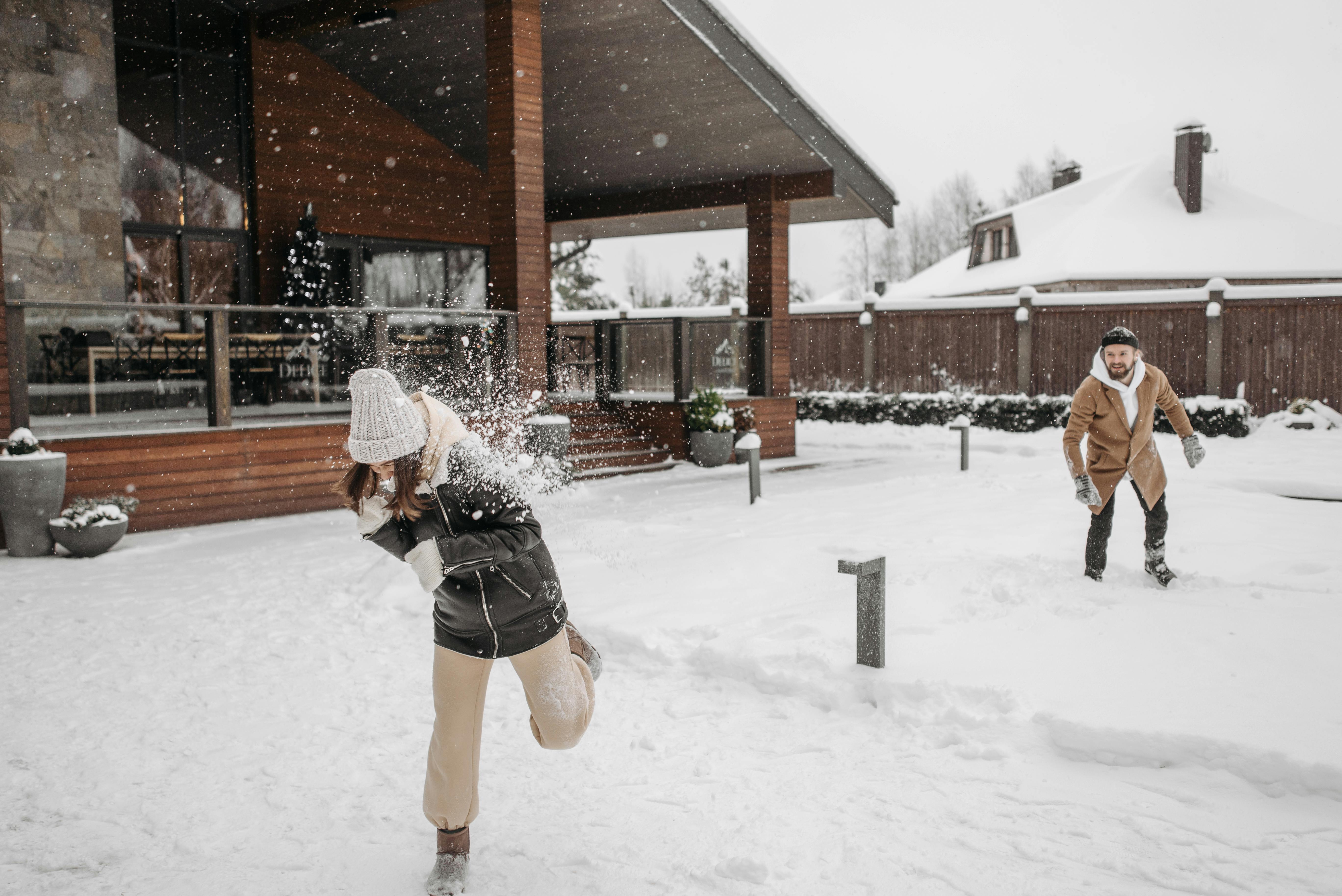 A Man and Woman Playing Snow Outside the House · Free Stock Photo