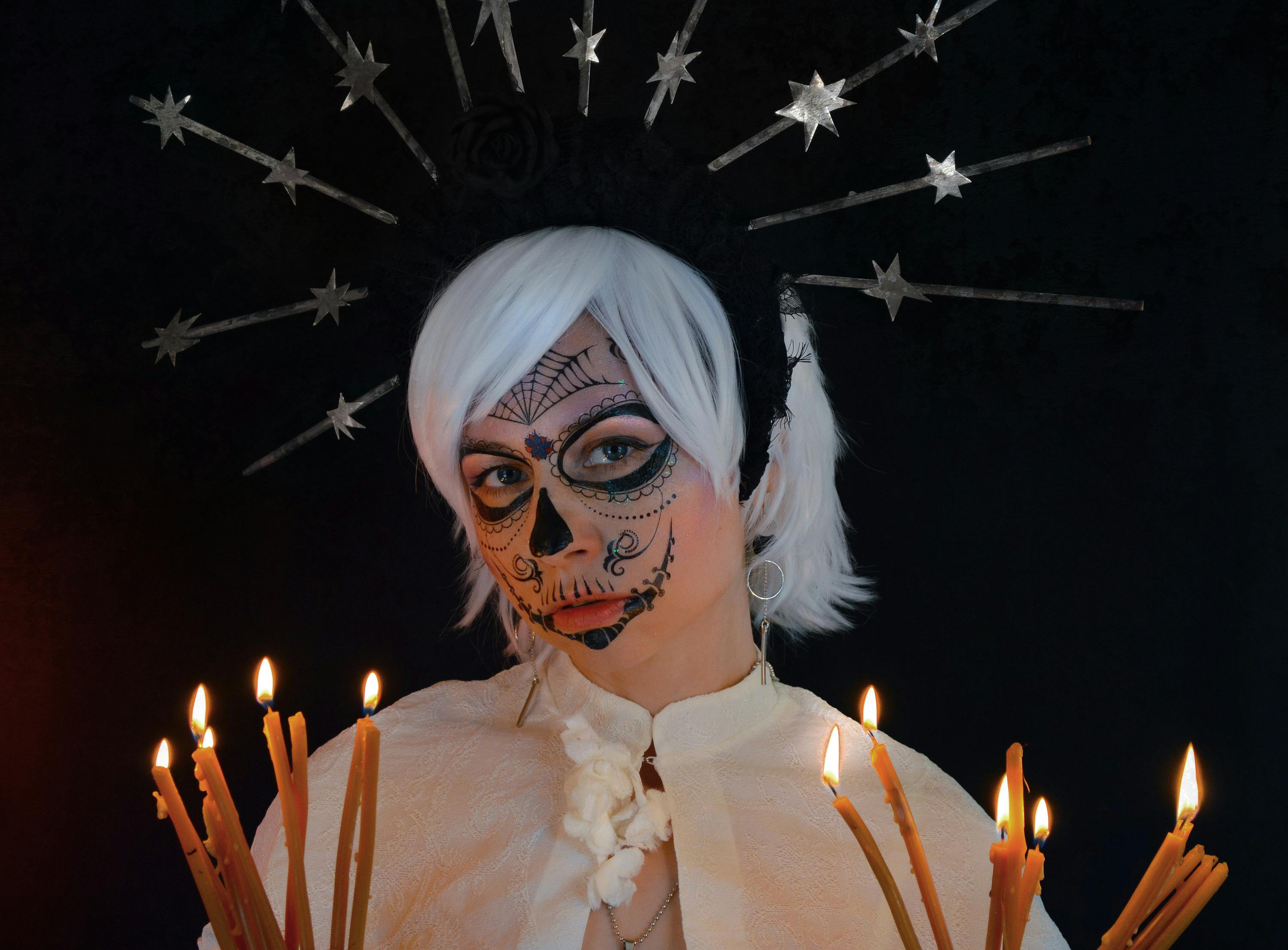 Young female magician with face art and burning candles in hands in ...