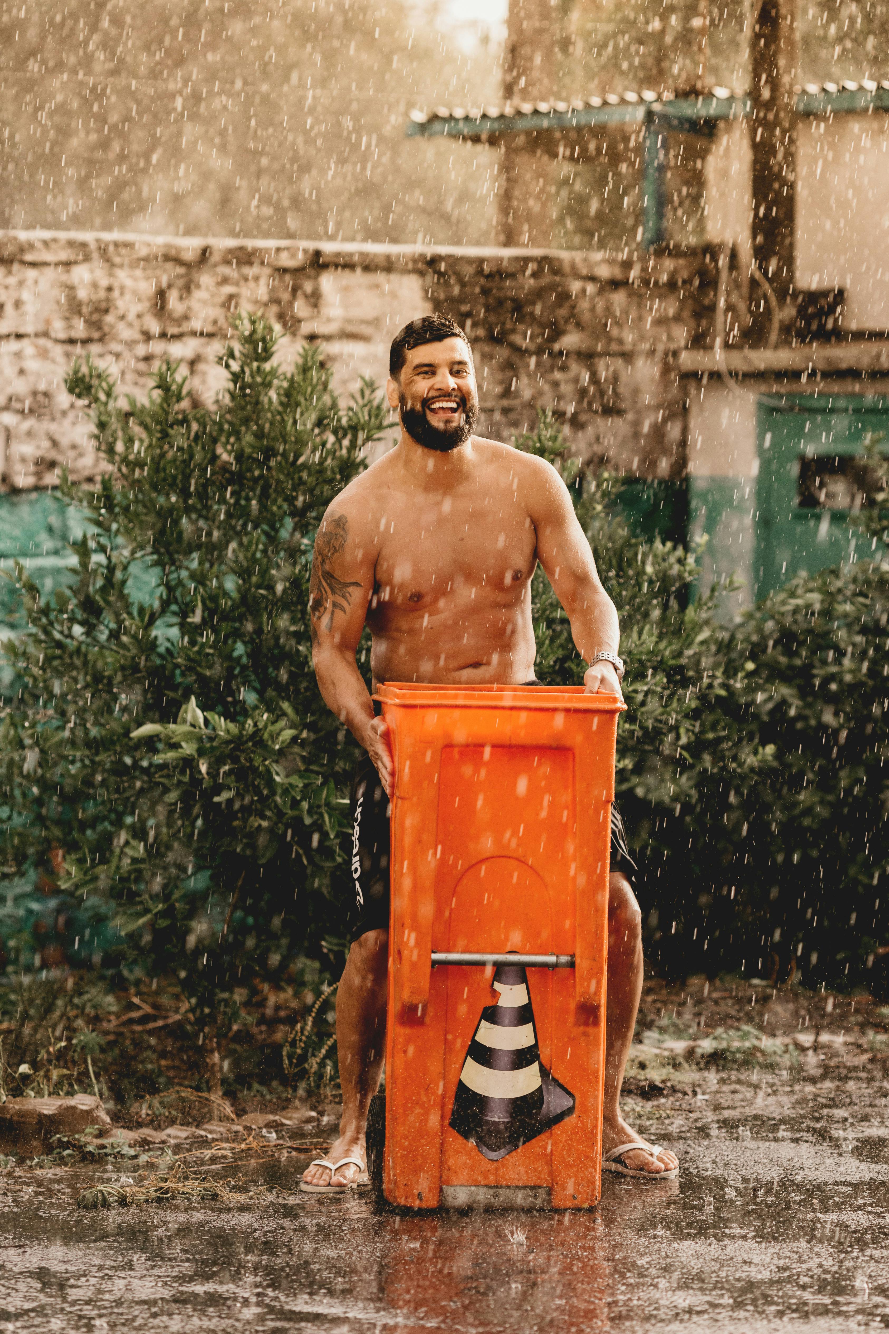 Cheerful shirtless ethnic man with trash can on street · Free Stock Photo