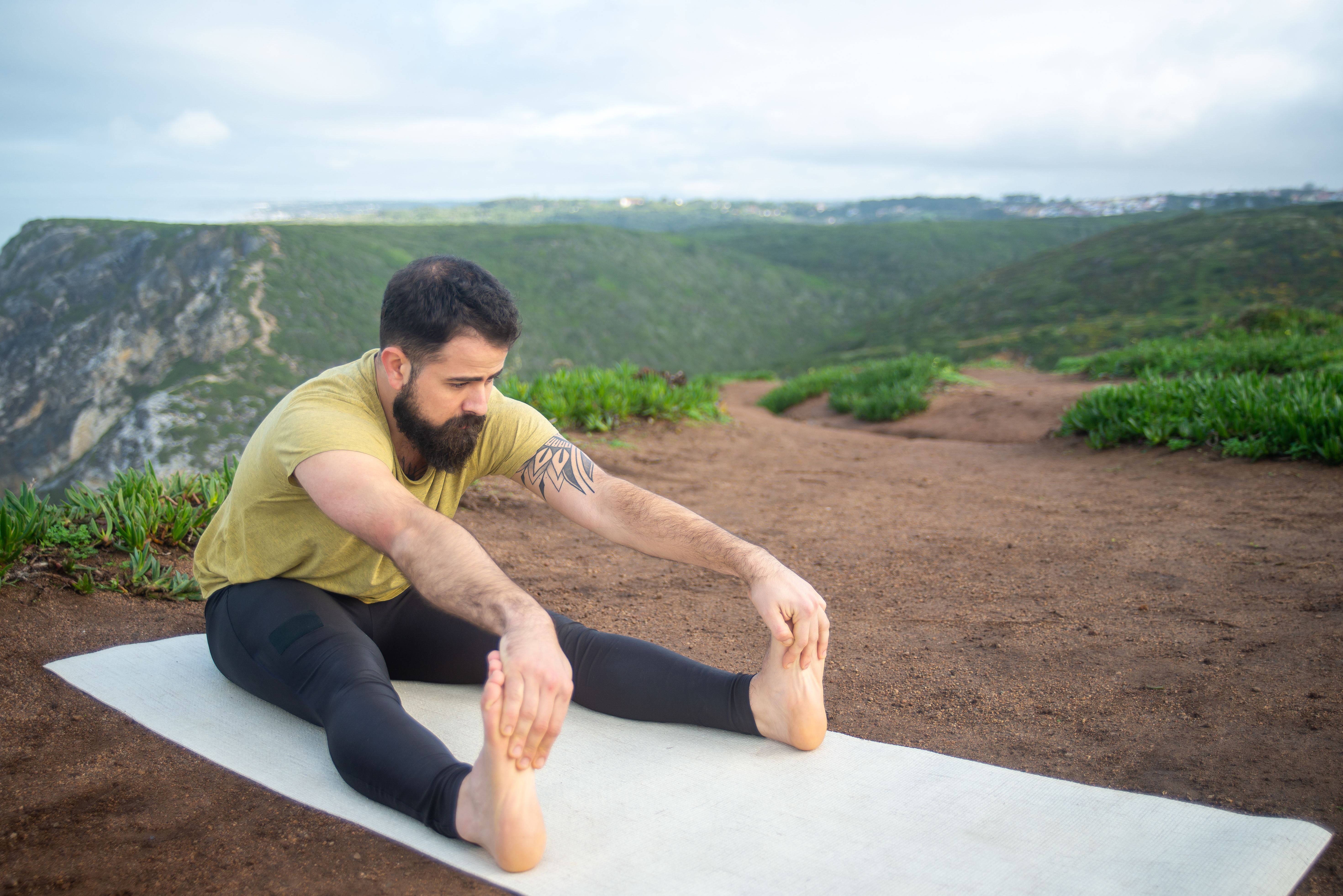 A Man Stretching while Sitting on a Yoga Mat · Free Stock Photo