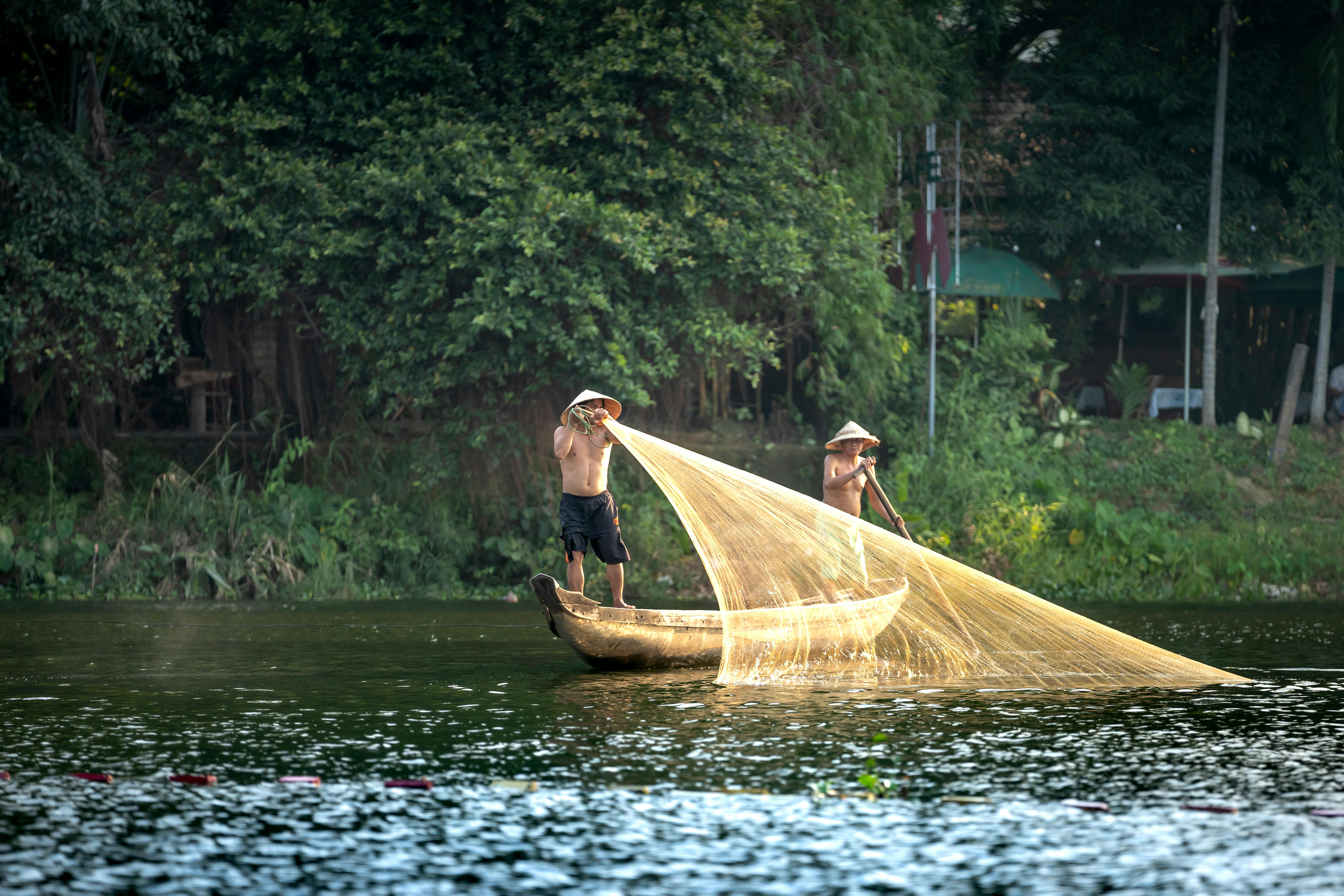 Anonymous fishermen catching fish in river from boat · Free Stock Photo