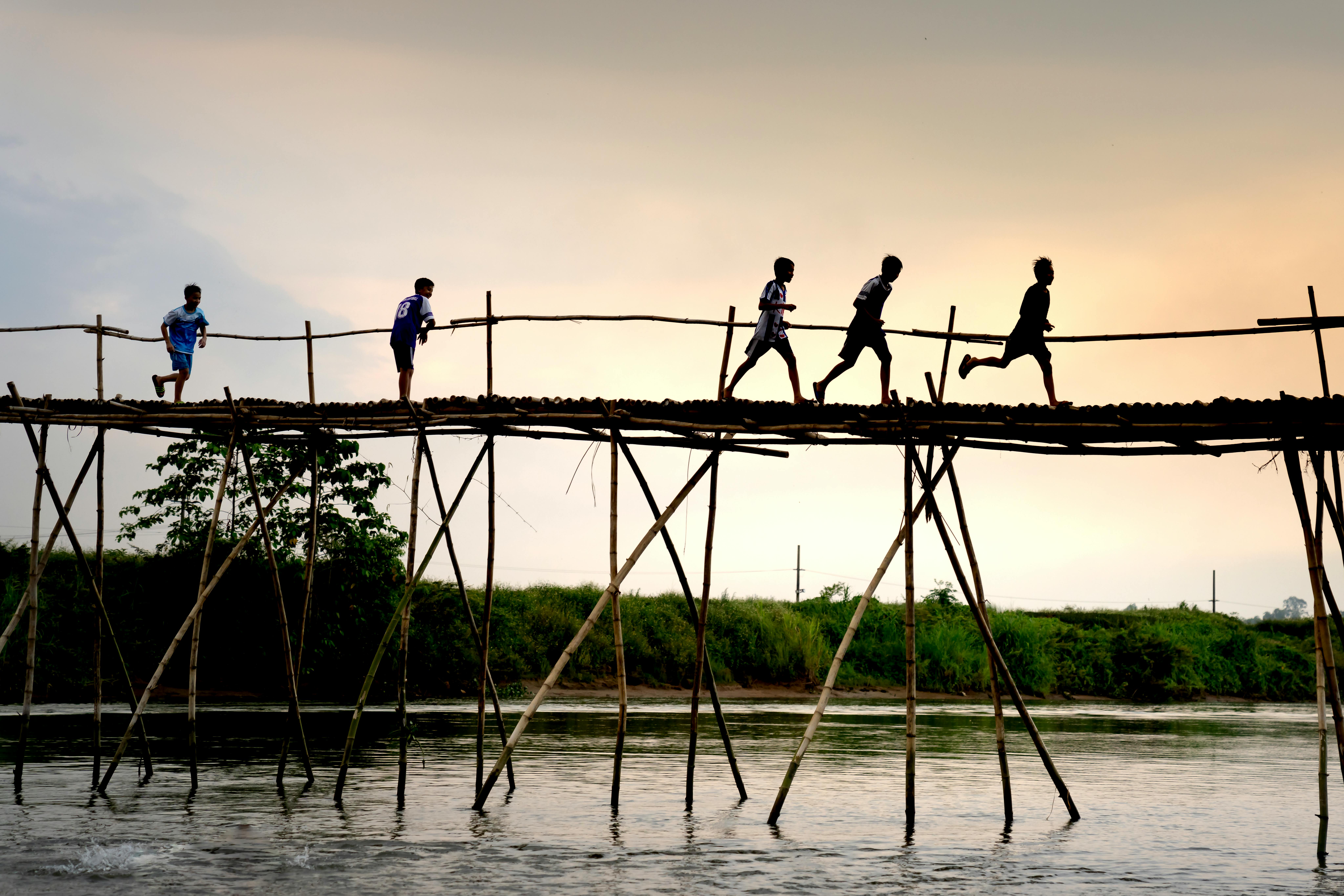 Anonymous ethnic children running on bridge over river in evening ...