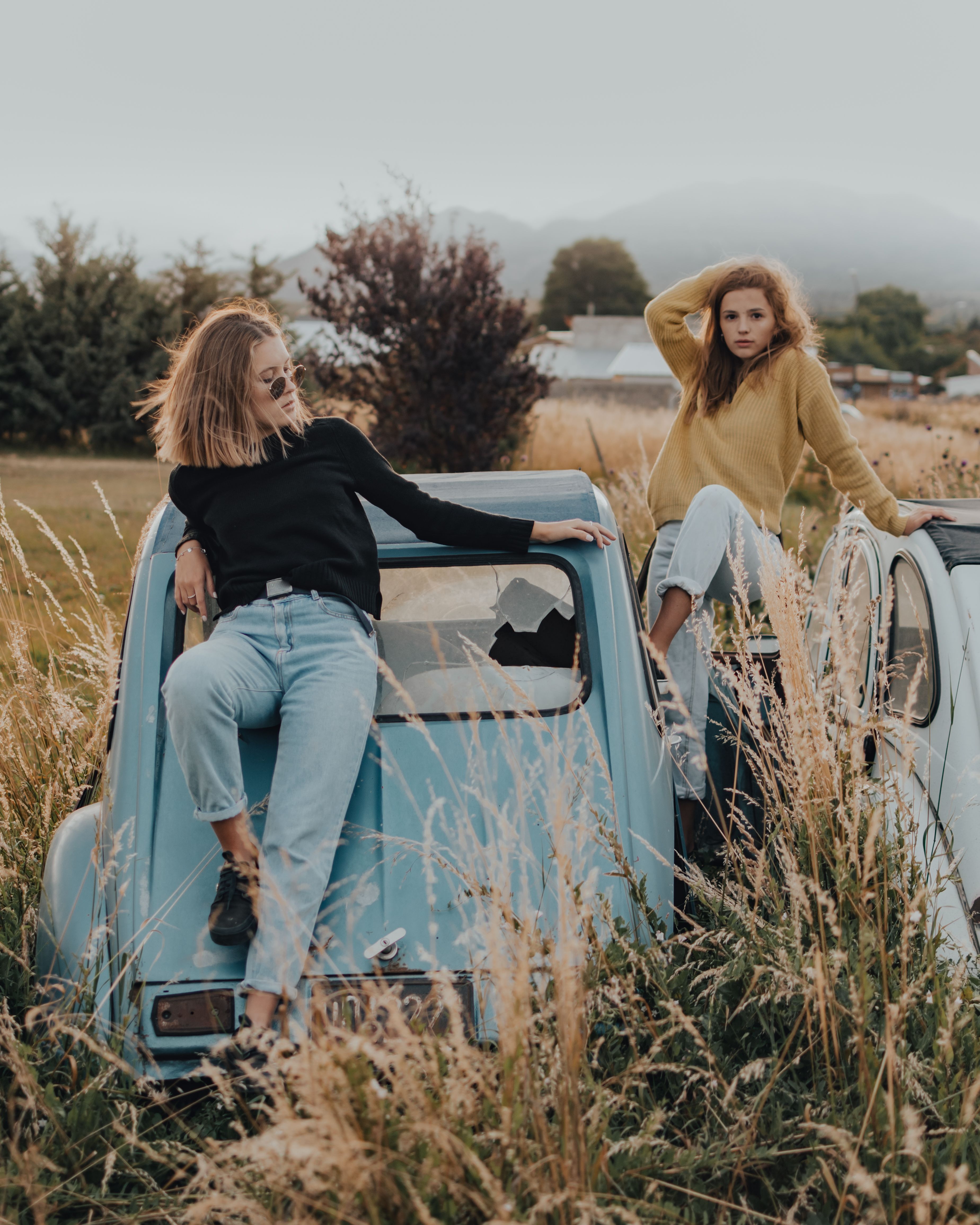 Women Wearing Sweaters Sitting on Abandoned Cars · Free Stock Photo