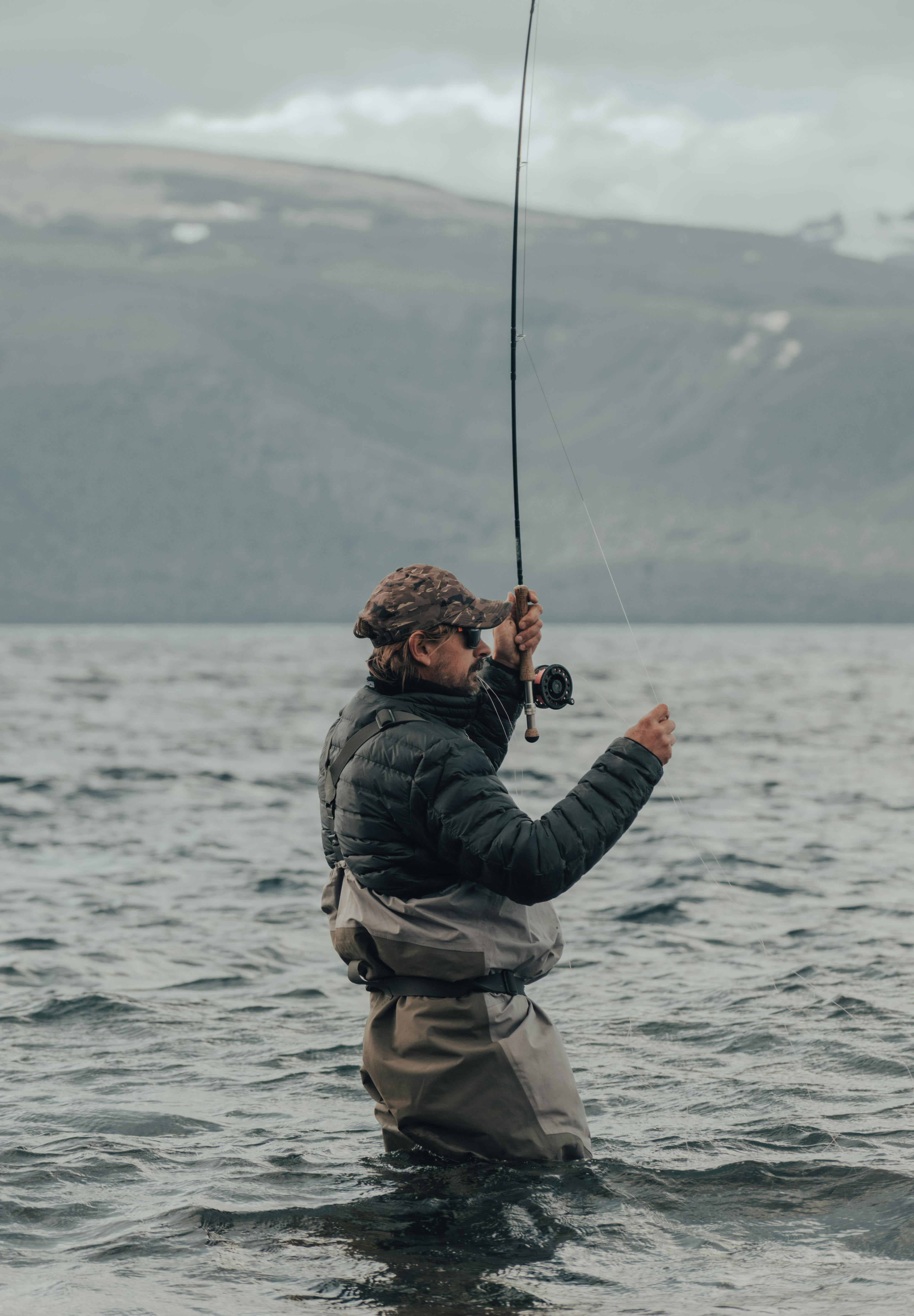 A Man in Black Jacket Standing in Body of Water Holding a Fishing Rod ...