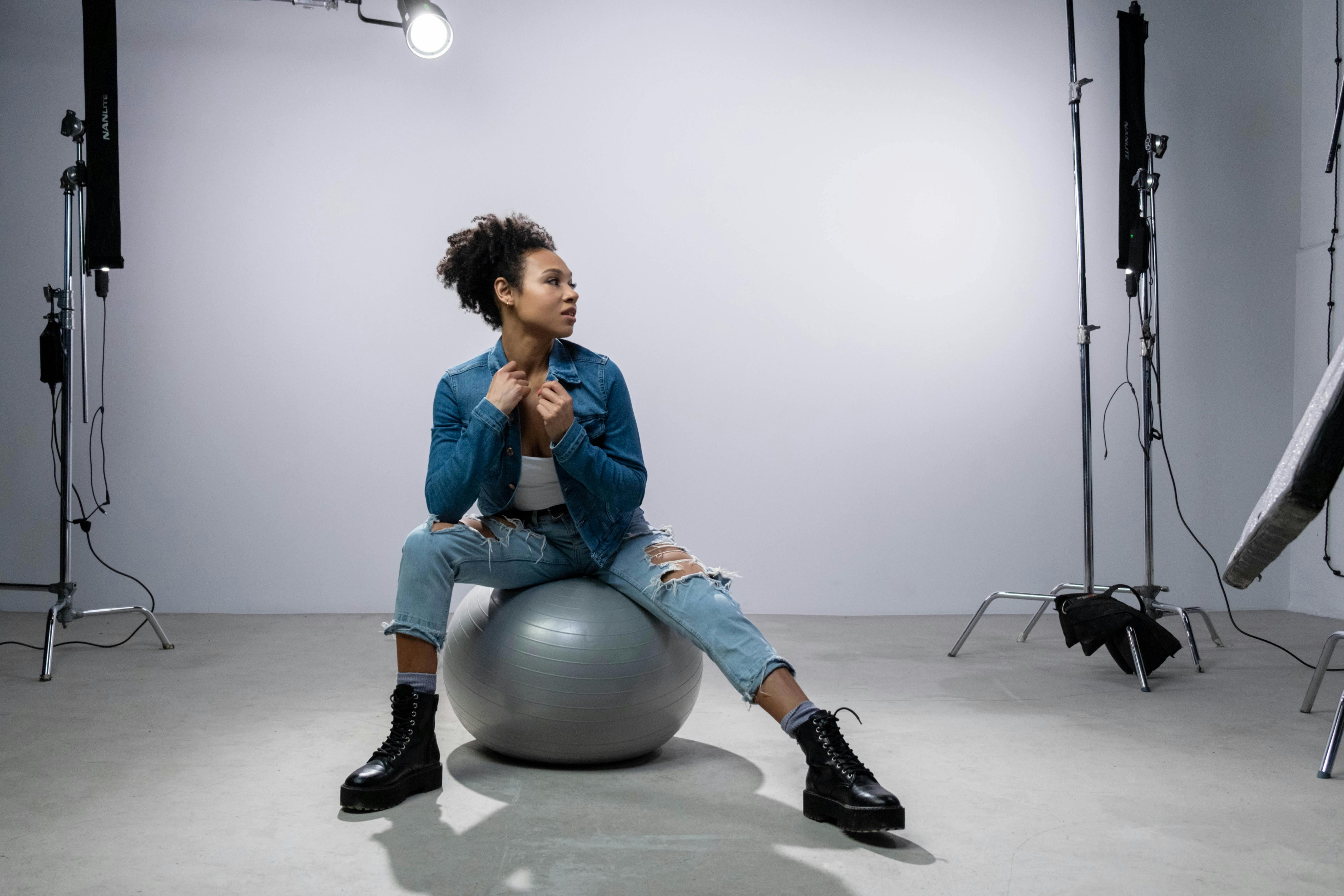A Woman in Blue Denim Jacket and Ripped Jeans Sitting on Exercise Ball ...