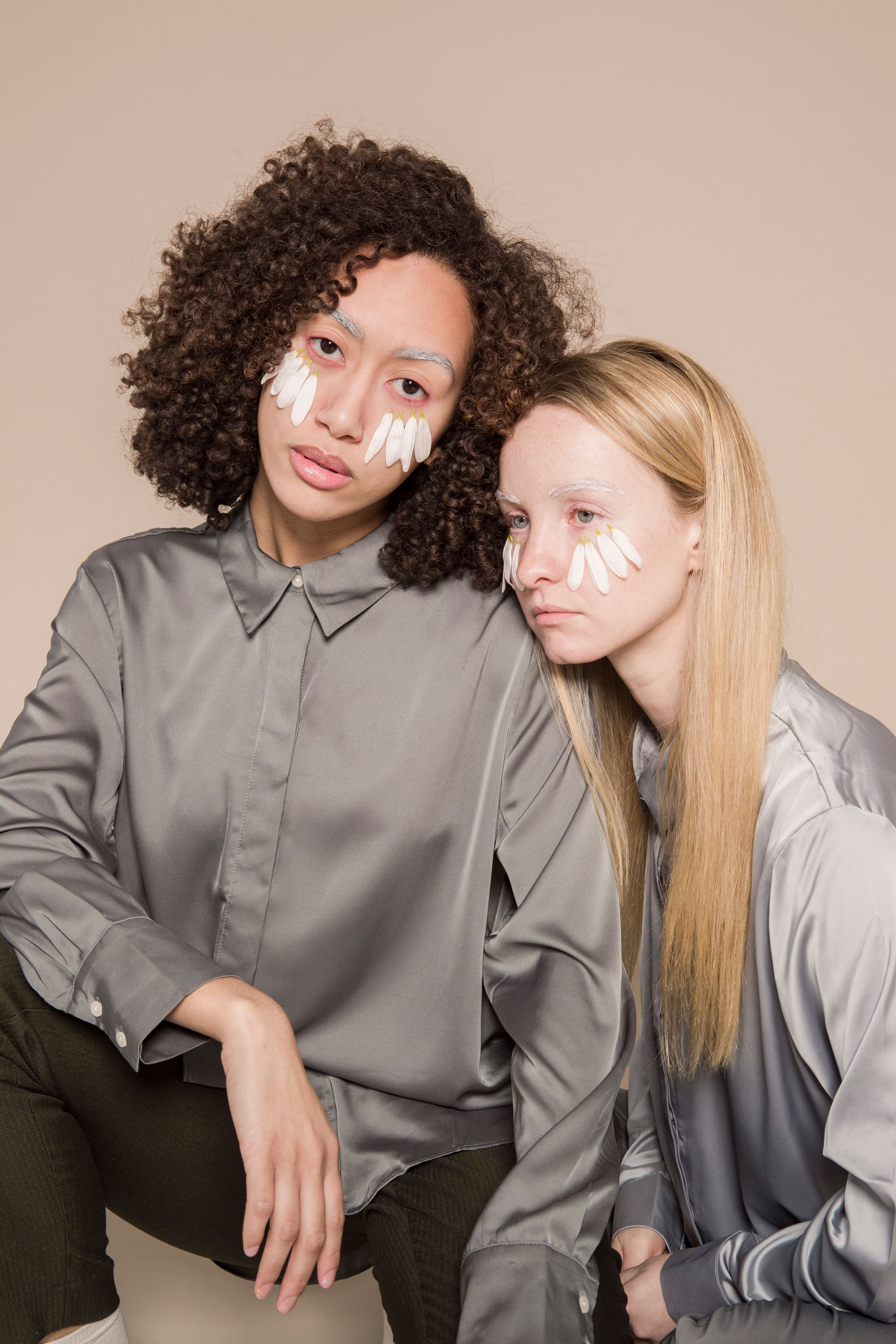 Feminine young ladies with flower petals on faces resting in studio ...